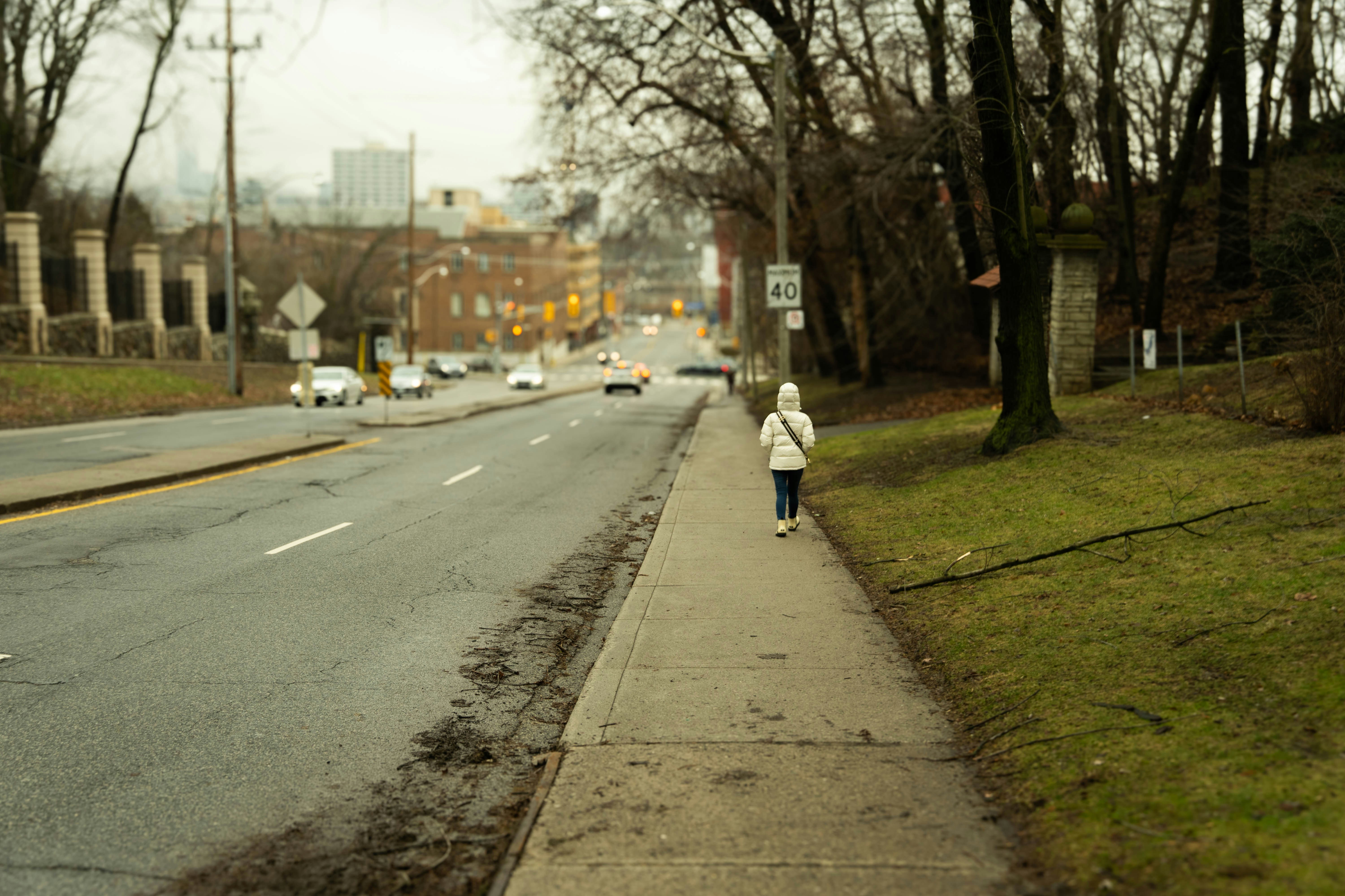 Sidewalk Solitude: A lone walker threads a quiet urban spine