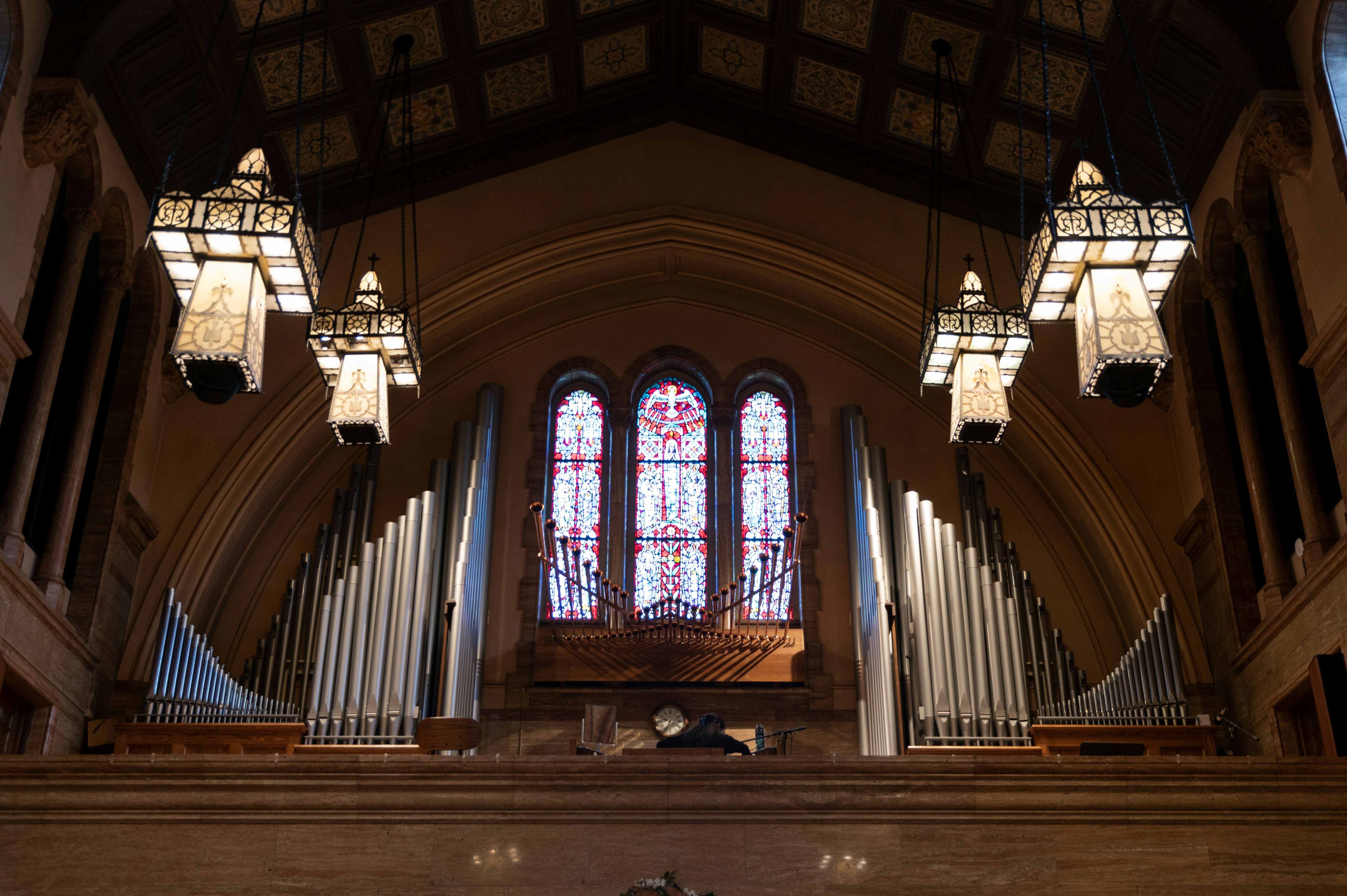 Grand organ pipes framed by ornate chandeliers in a dimly lit cathedral with stained glass windows.