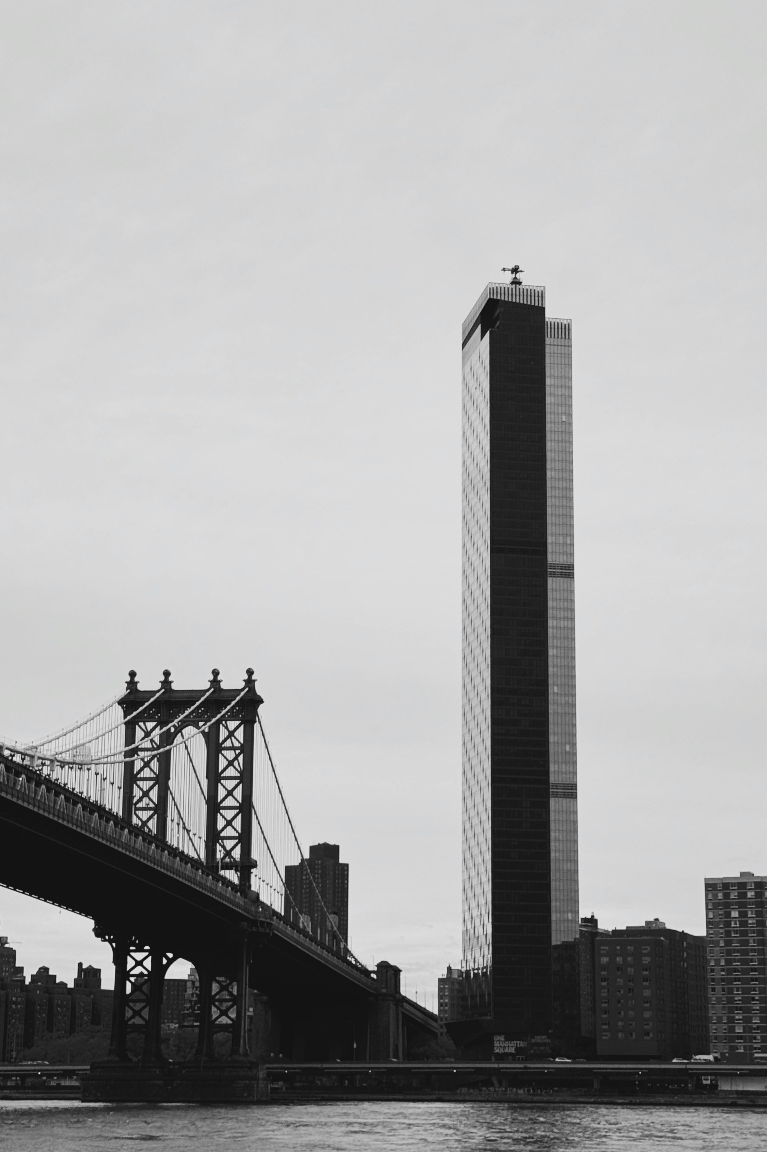 Monochrome Vanguard: The Narrow Glass Tower Rises Over a Classic Bridge