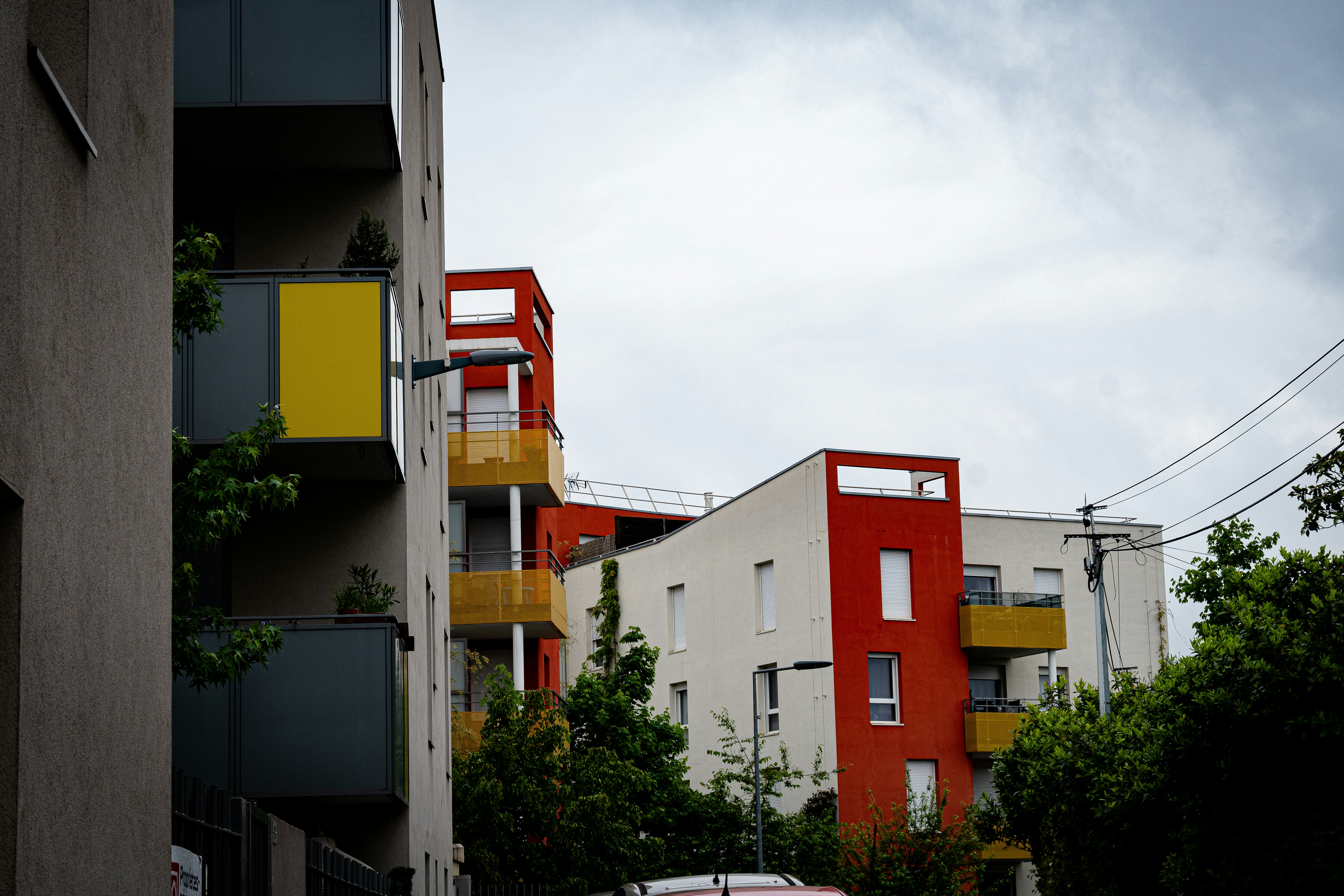 Vibrant apartment buildings featuring bold red, yellow, and gray accents, framed by lush greenery and an overcast sky.