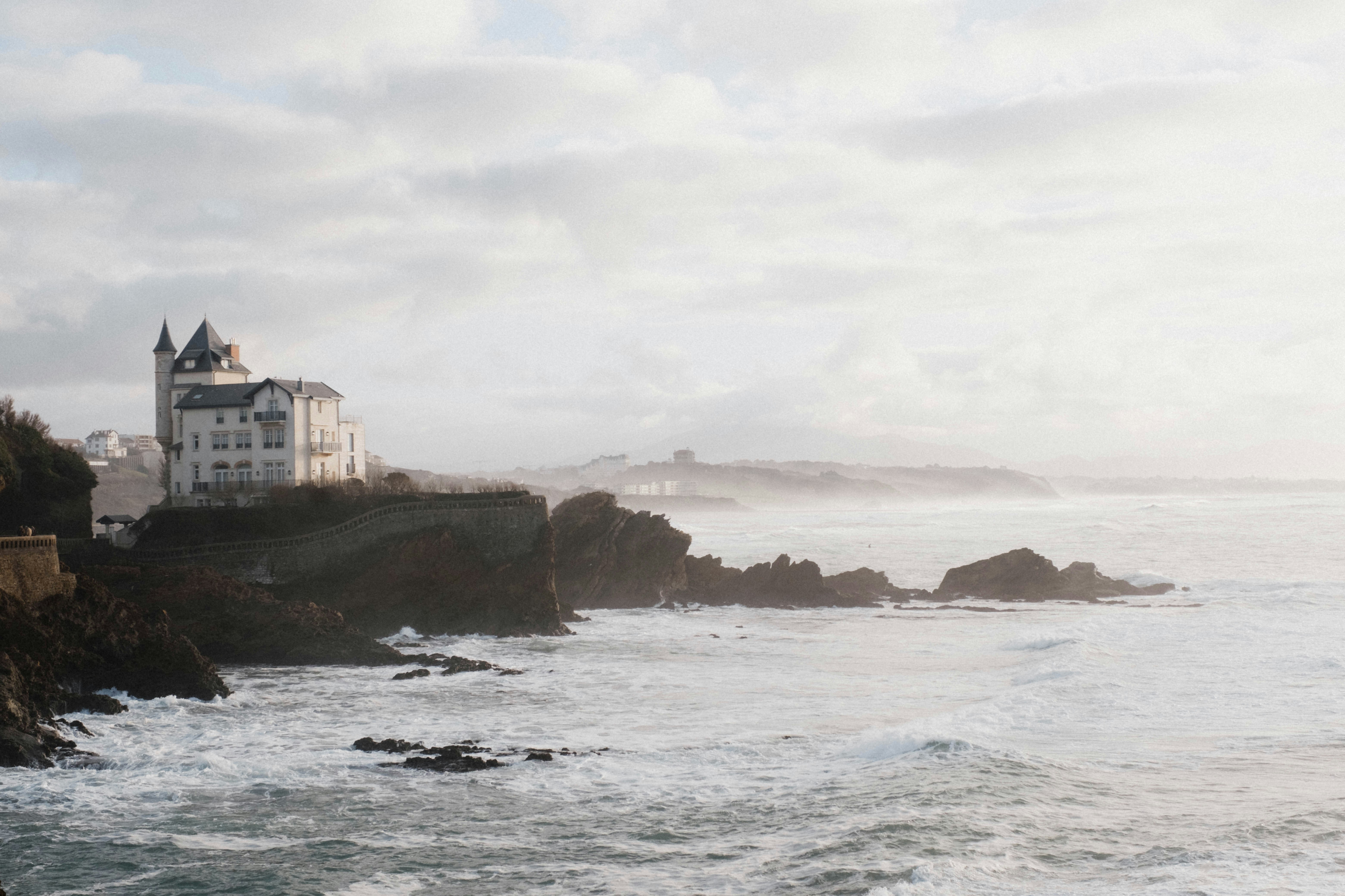 A large white building sitting on top of a cliff next to the ocean ...