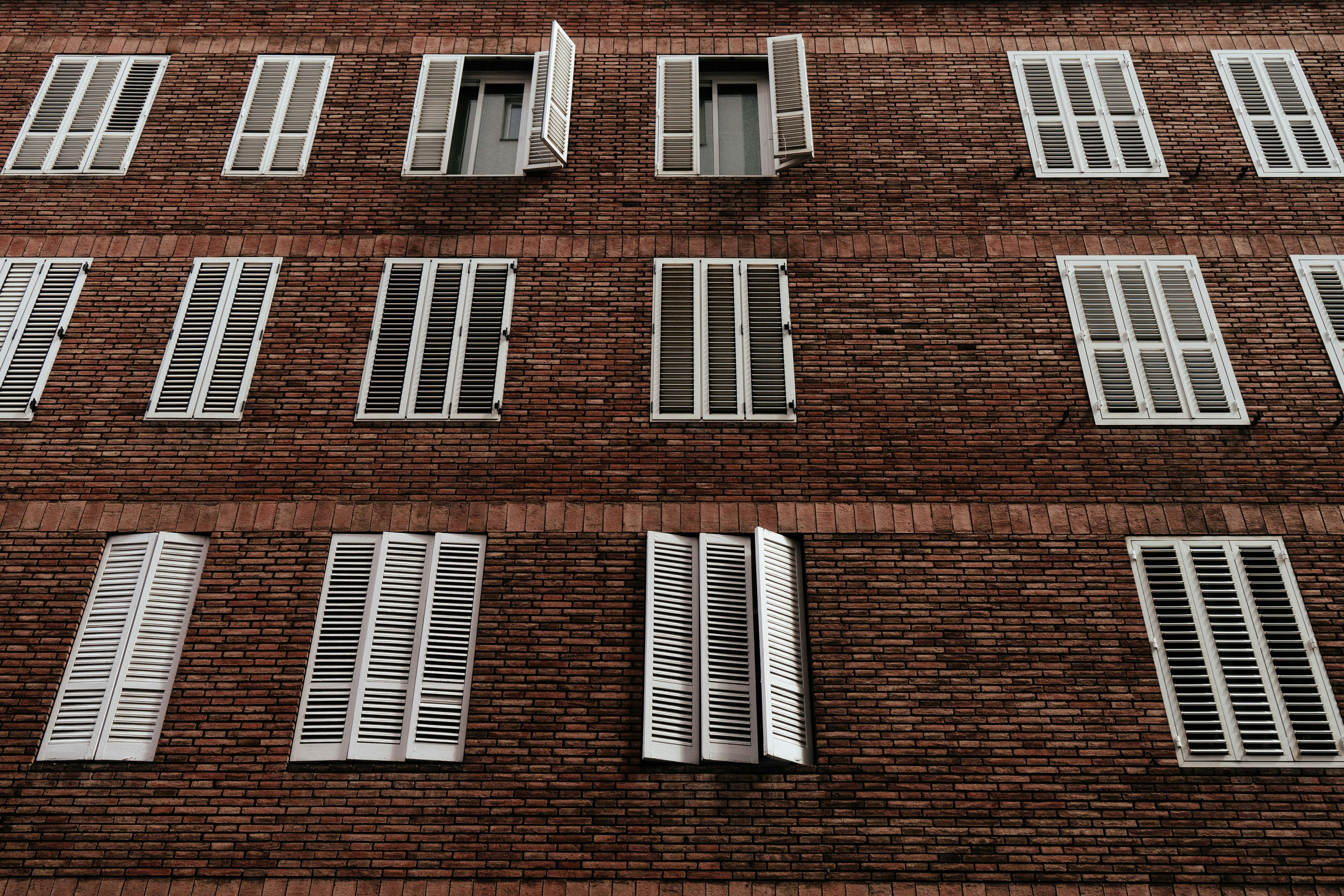 A tall brick building with white windows and shutters photo – Free ...