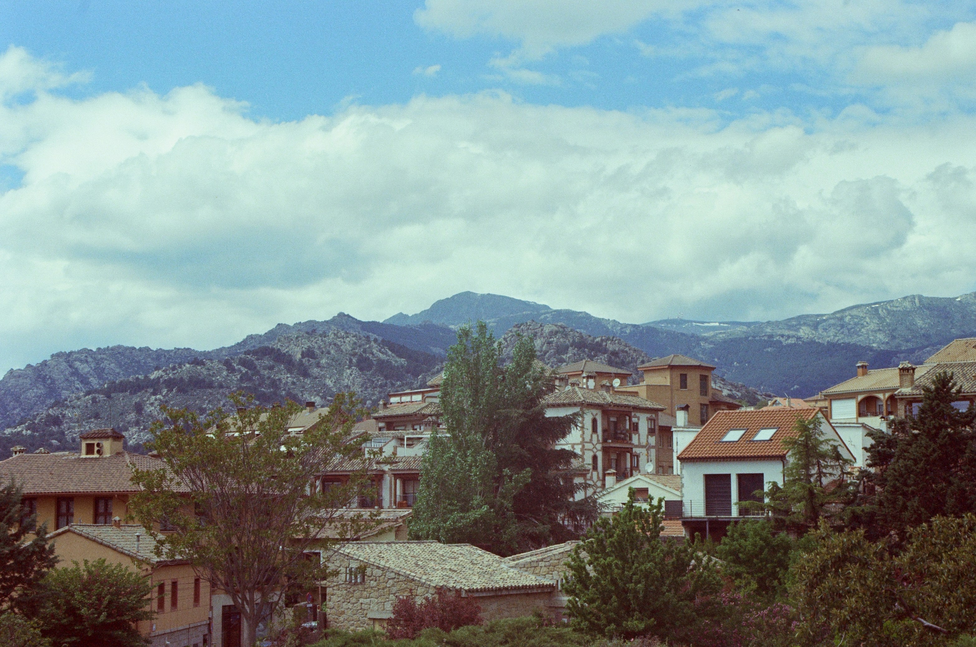 Town nestled among lush greenery with distant mountains under a partly cloudy sky.