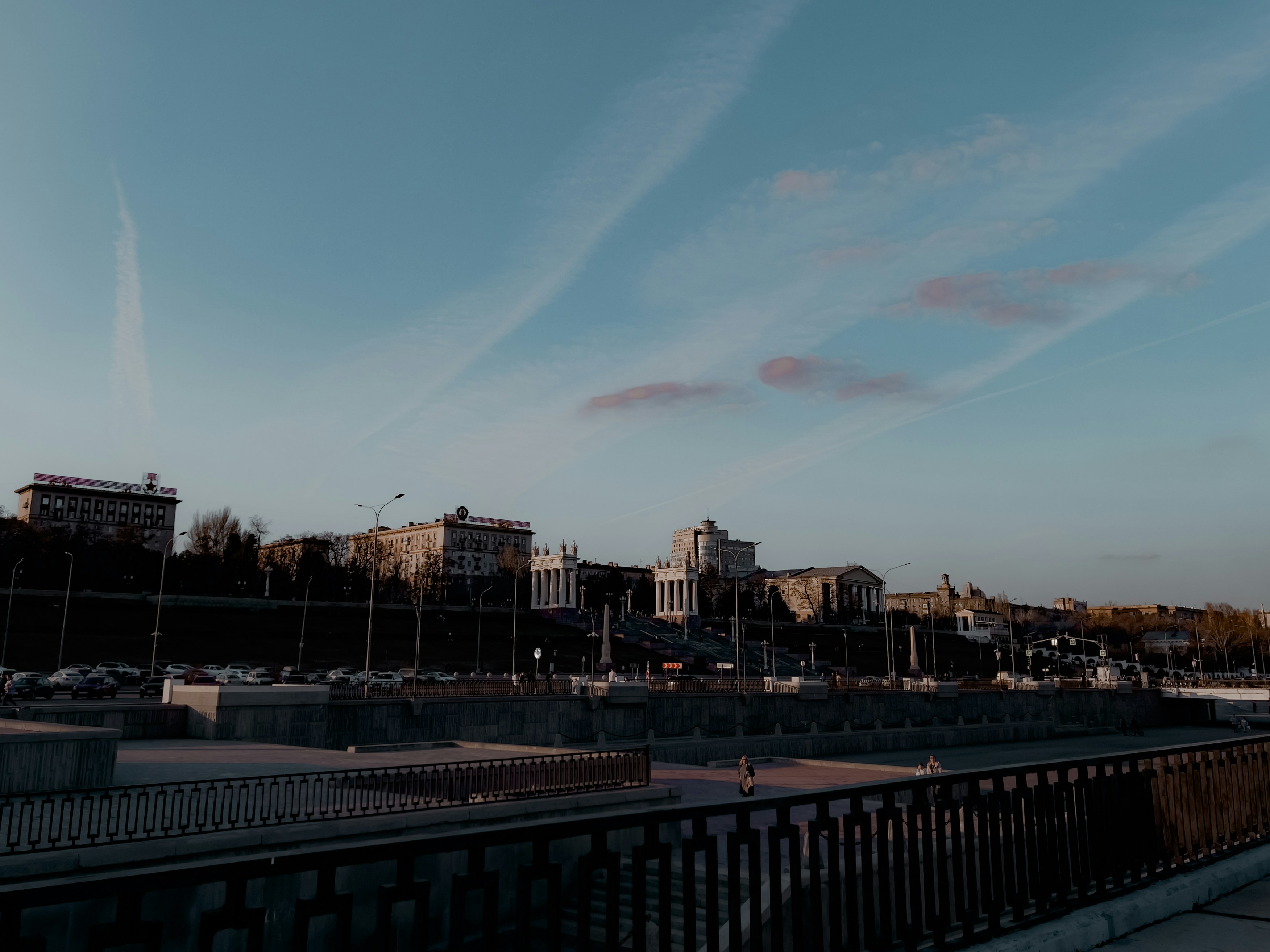 City skyline viewed from a bridge under a dusky blue sky with scattered clouds.