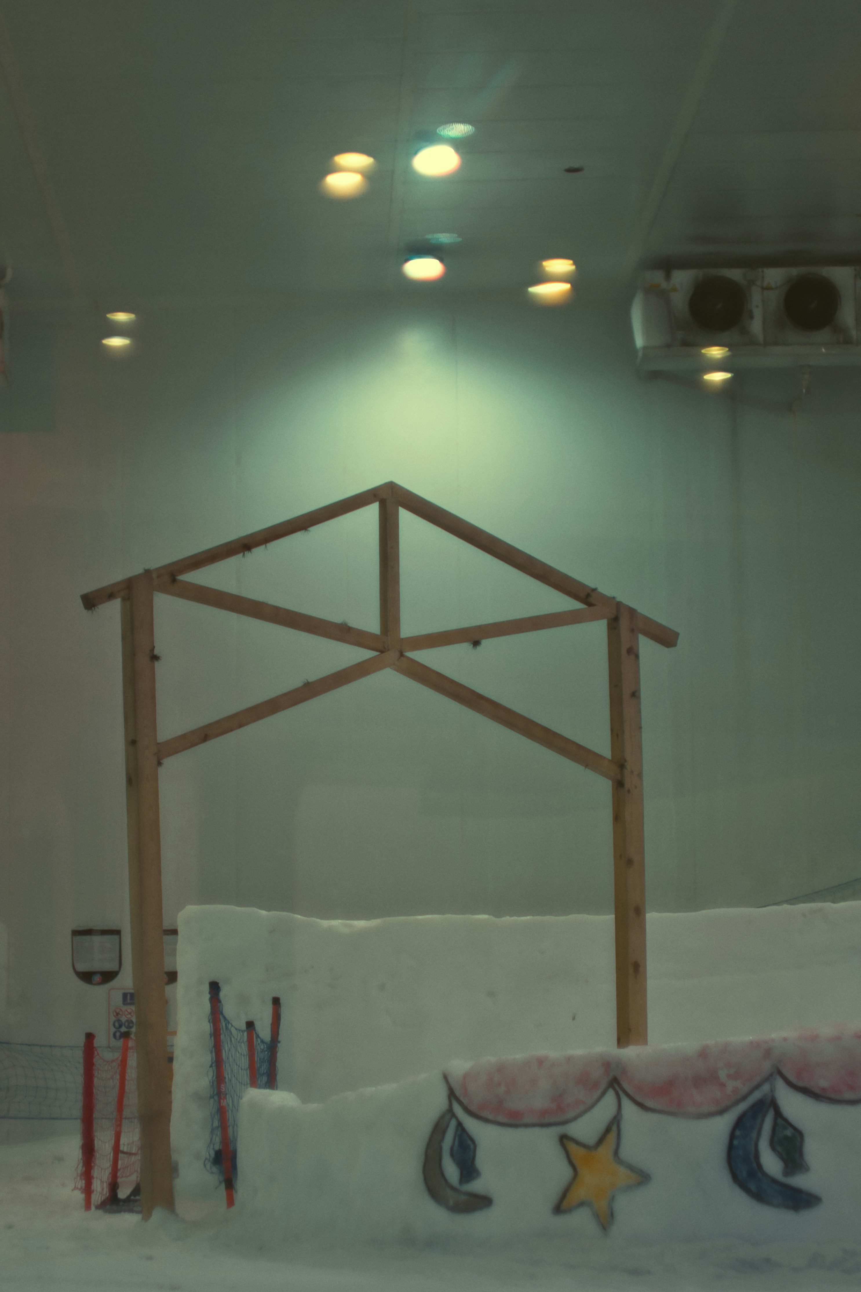Indoor snow park photographed with a tall wooden arch framing a snow ramp. The snow wall is painted with moons and stars under soft overhead lighting.