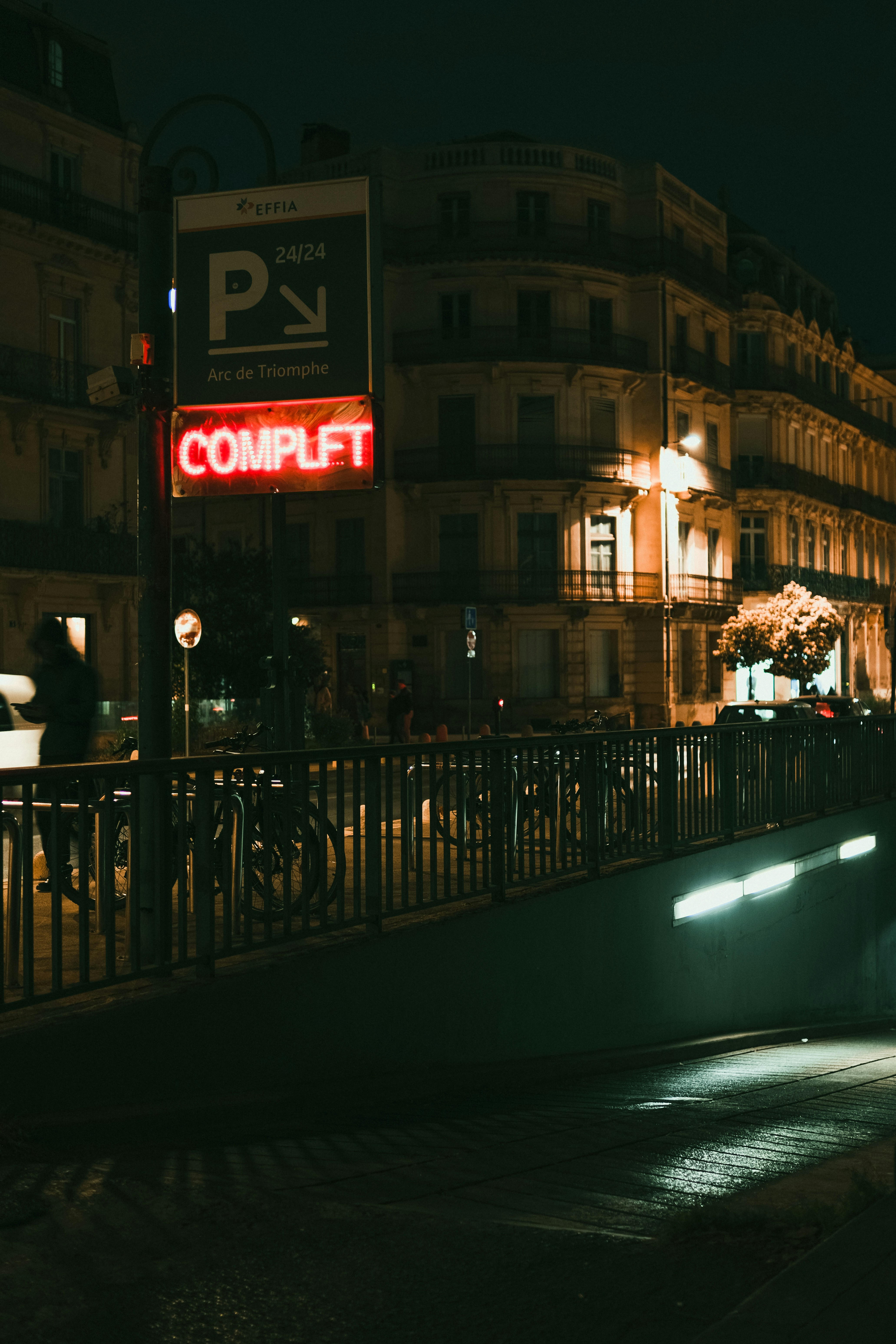 Illuminated street scene with a 'Complet' sign and softly lit buildings at night.