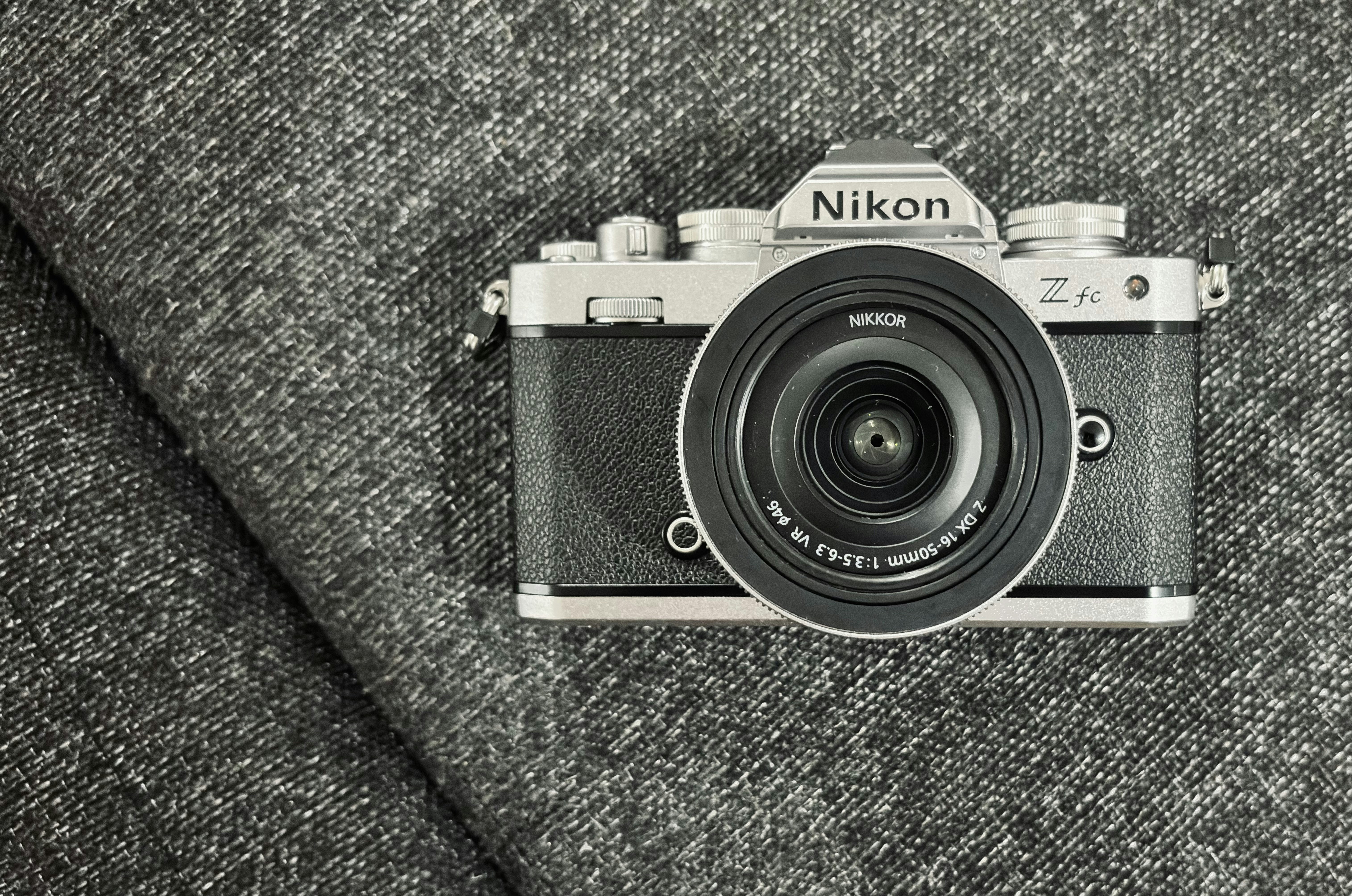 Vintage Nikon Z fc camera with a compact lens rests on a textured gray fabric surface.