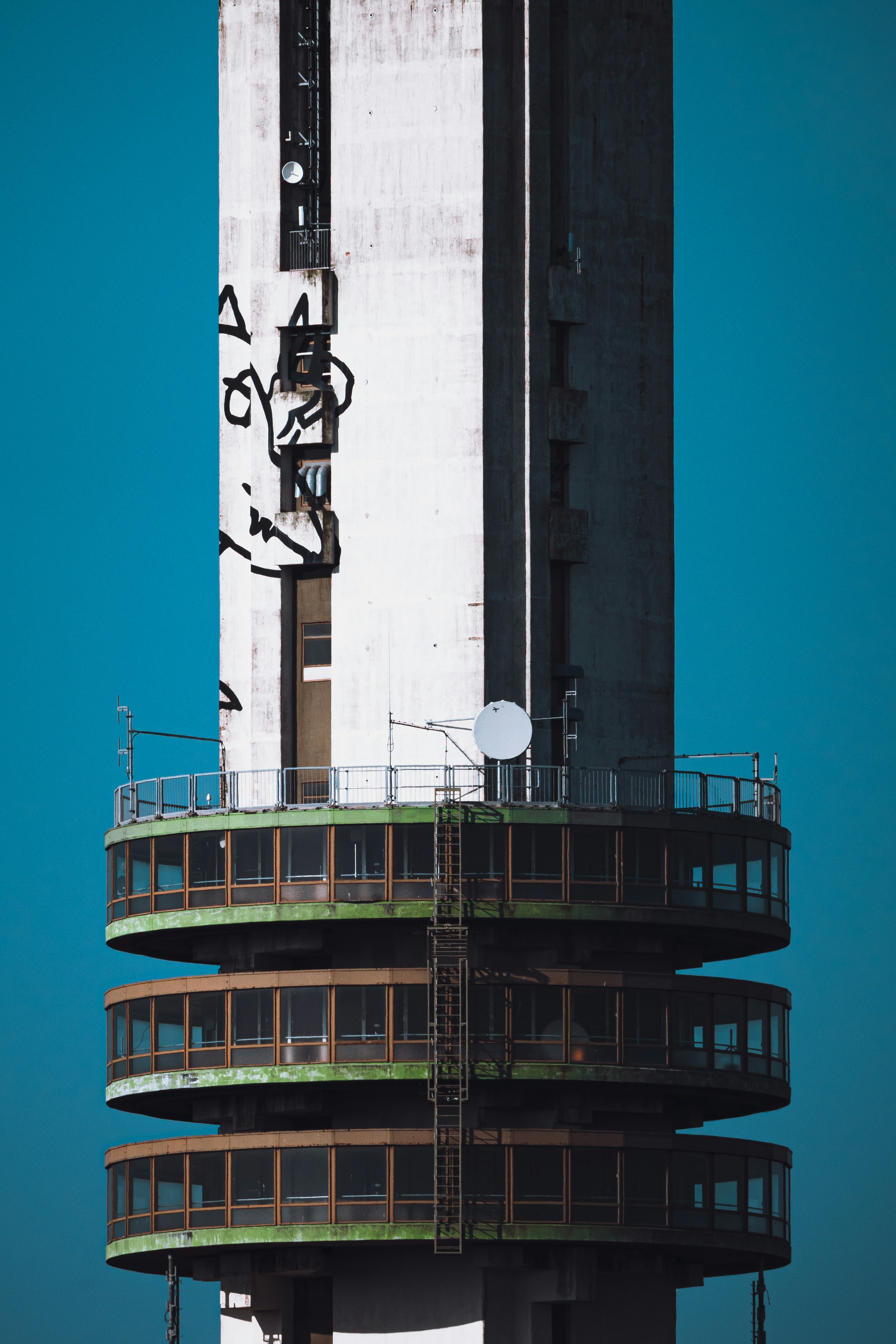 Rings and Rails: A Weathered Control Tower Reaches Toward a Cerulean Sky