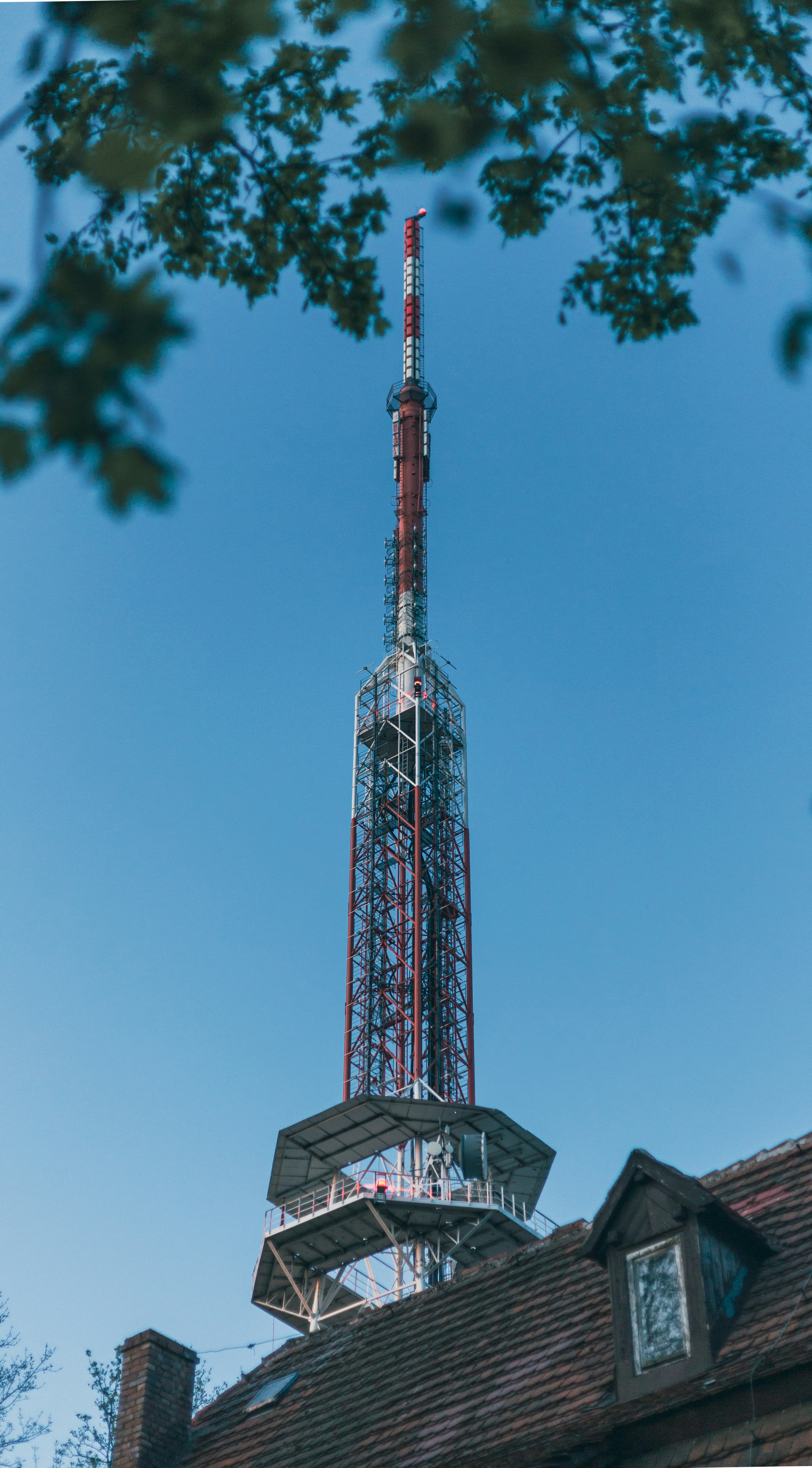 Apex of Steel Mast Rising Over a Tile Roof Against a Clear Blue Sky