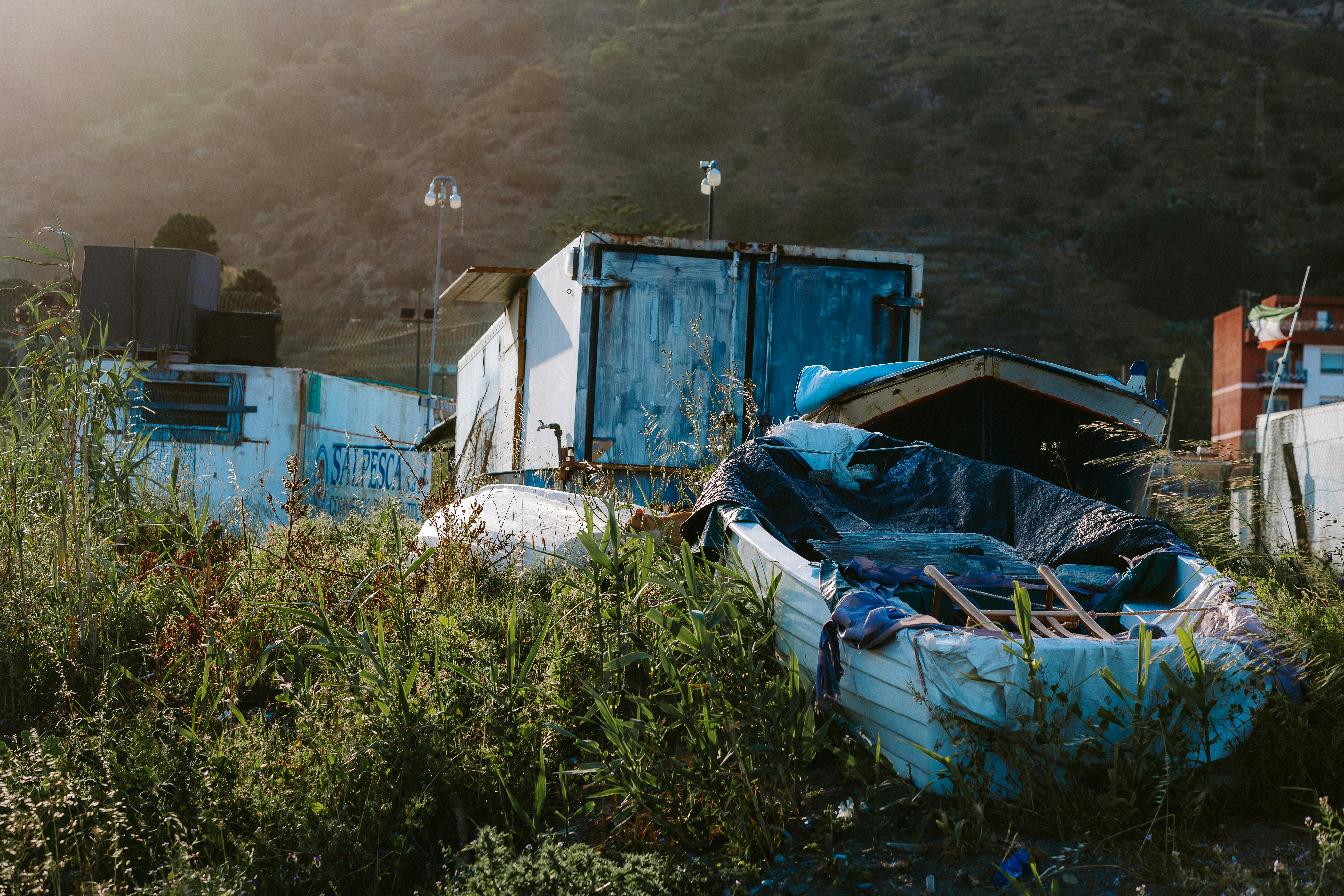 Blue Hull in Sunlit Decay: A Quiet Boatyard Among Weeds