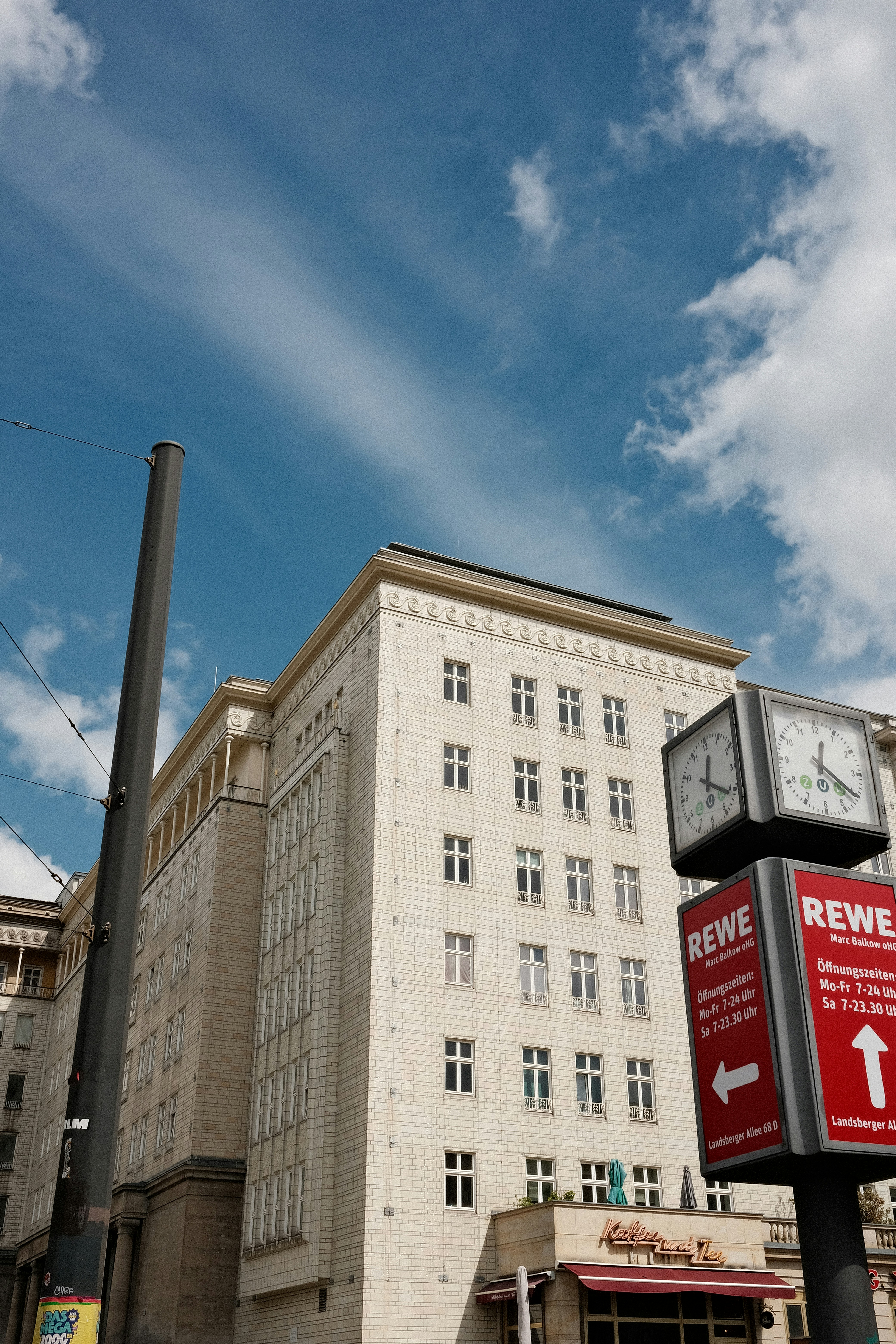 Timekeeper on a European Street: Sunlit Facade, Clock Sign, and Red Storefronts