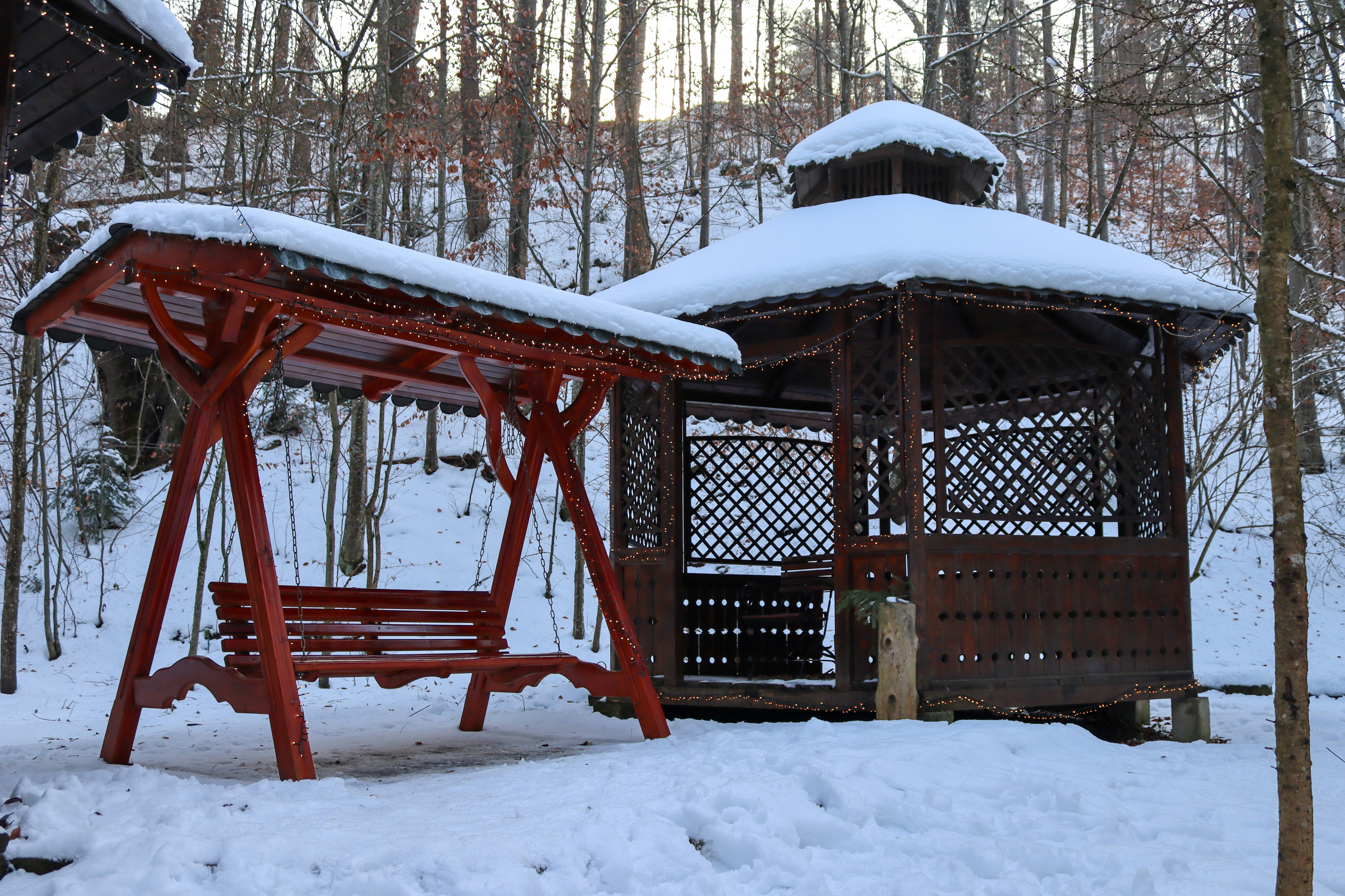Red Swing Shelter Beside a Snow-Covered Gazebo in a Quiet Winter Clearing