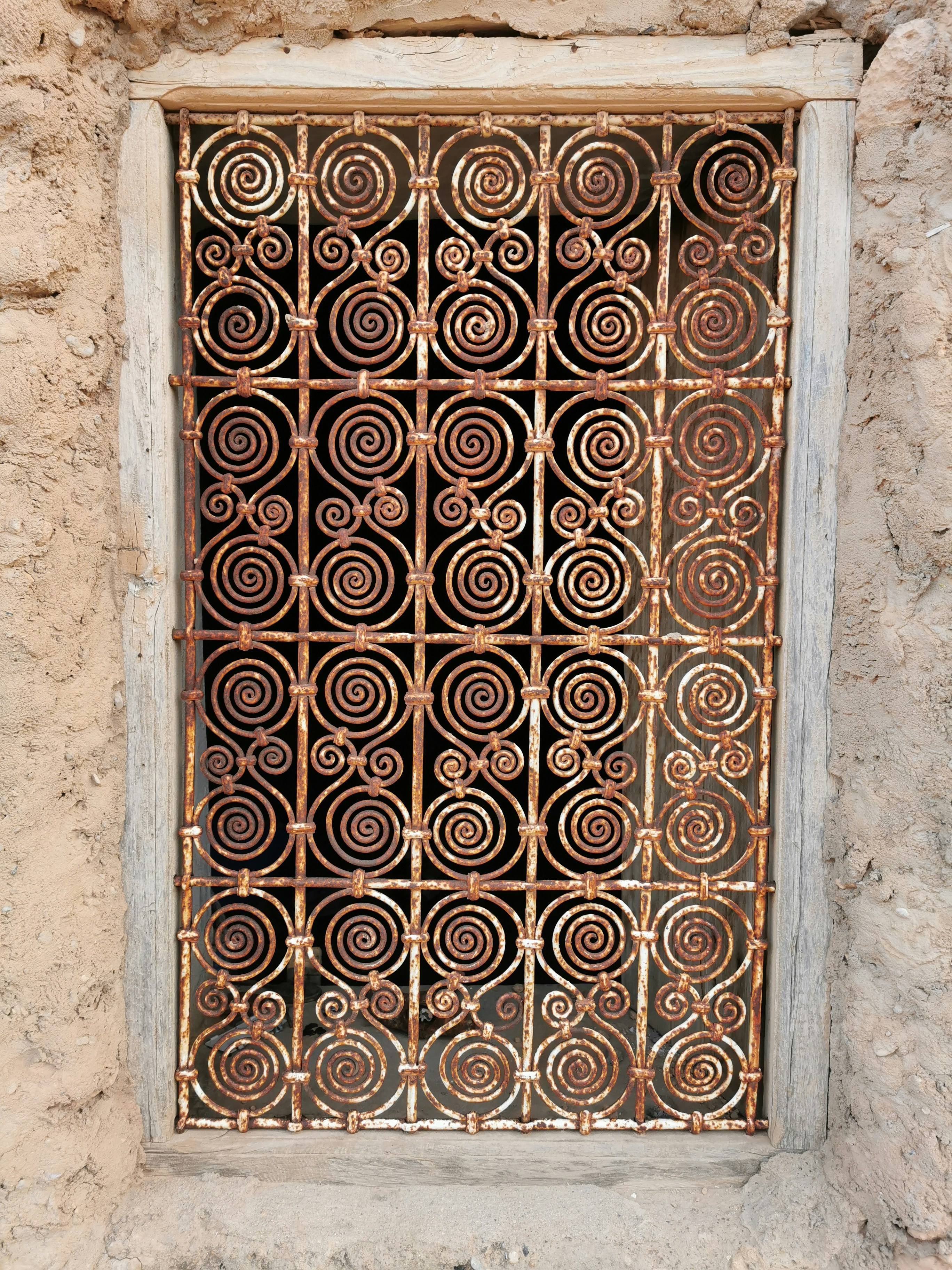 Rust-Copper Spirals Framing a Mud-Walled Window