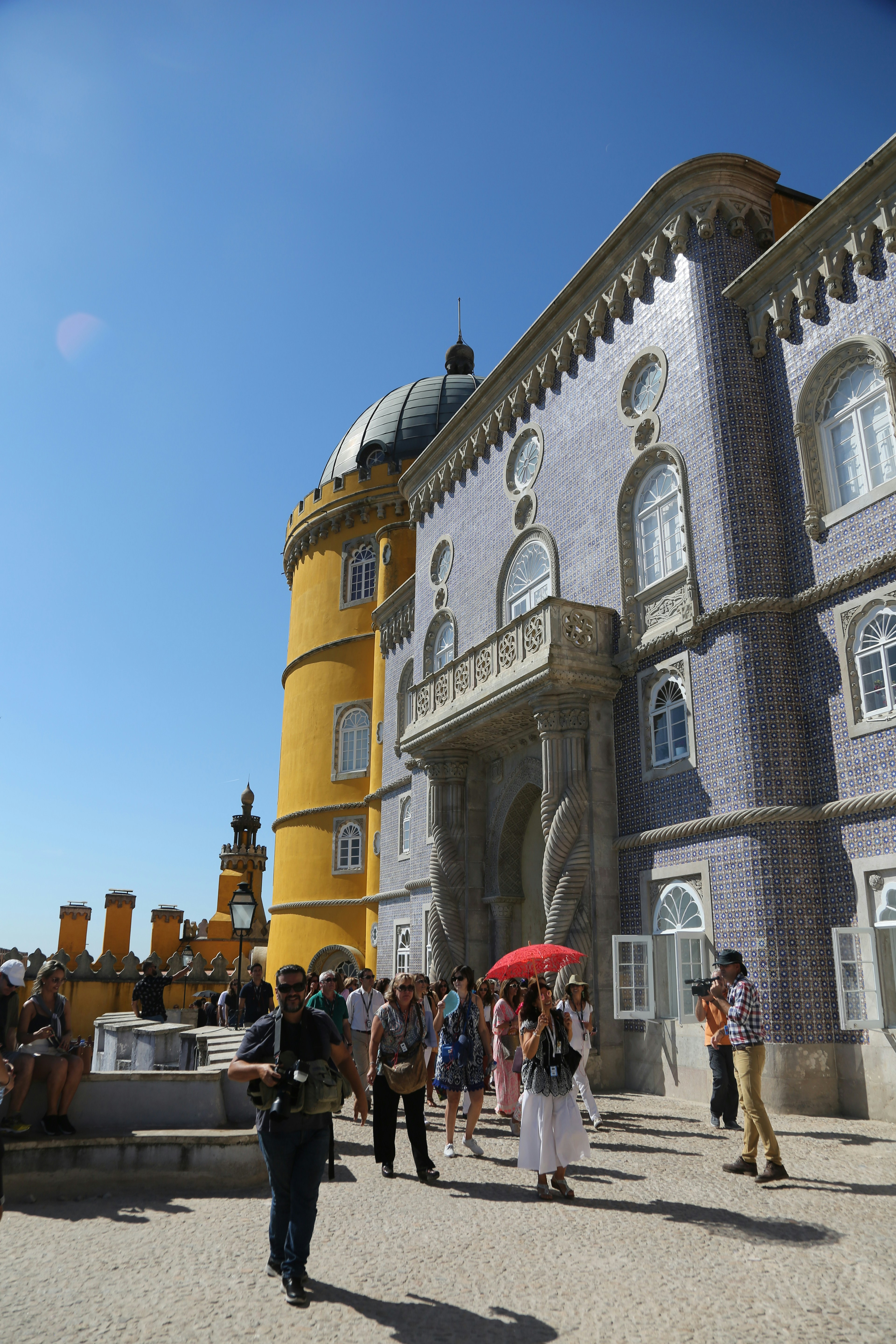 Sunlit Courtyard at Pena Palace: Tourists Amid Purple Tiles and a Bright Yellow Turret