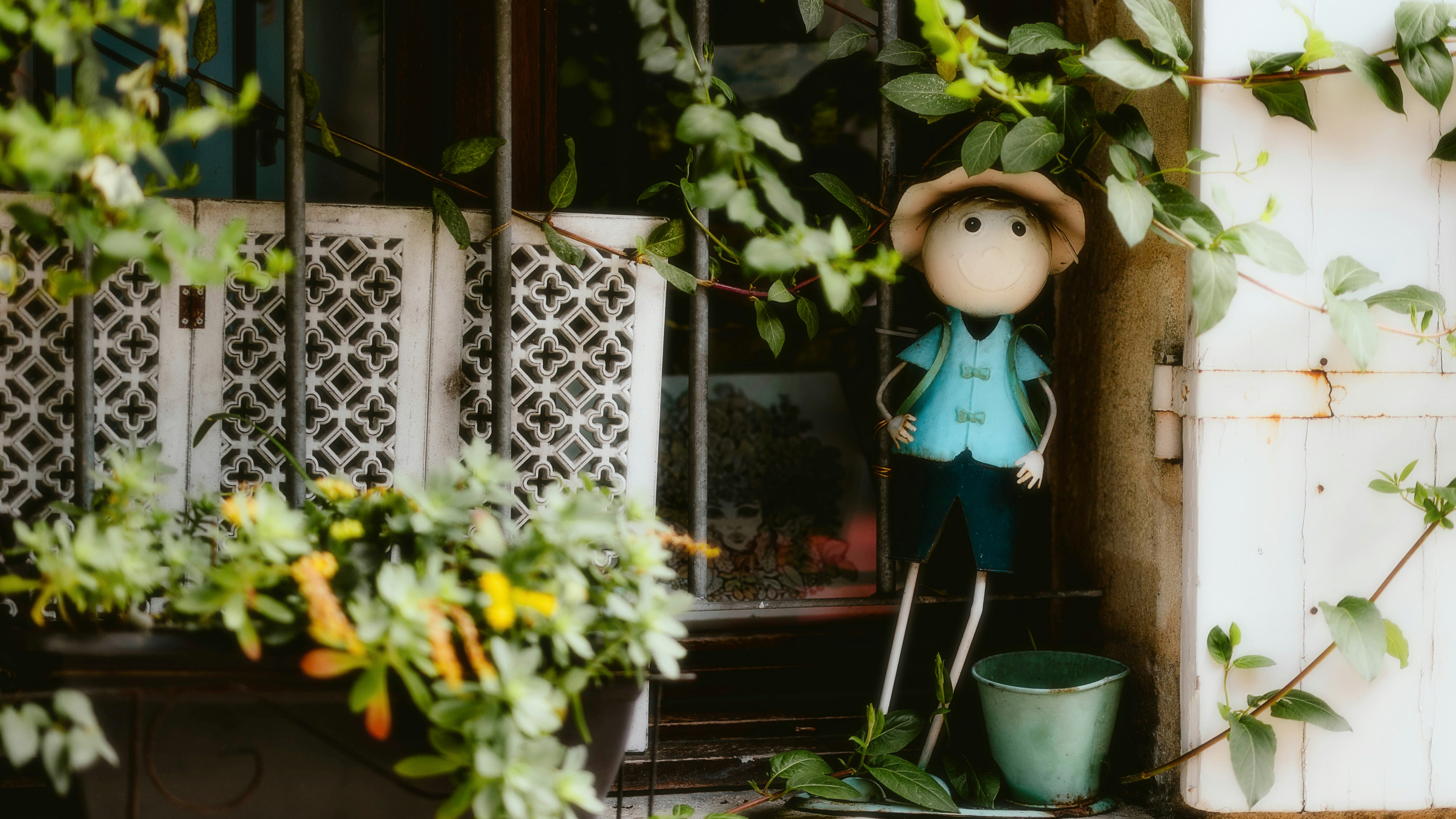 a doll in a hat standing next to a potted plant