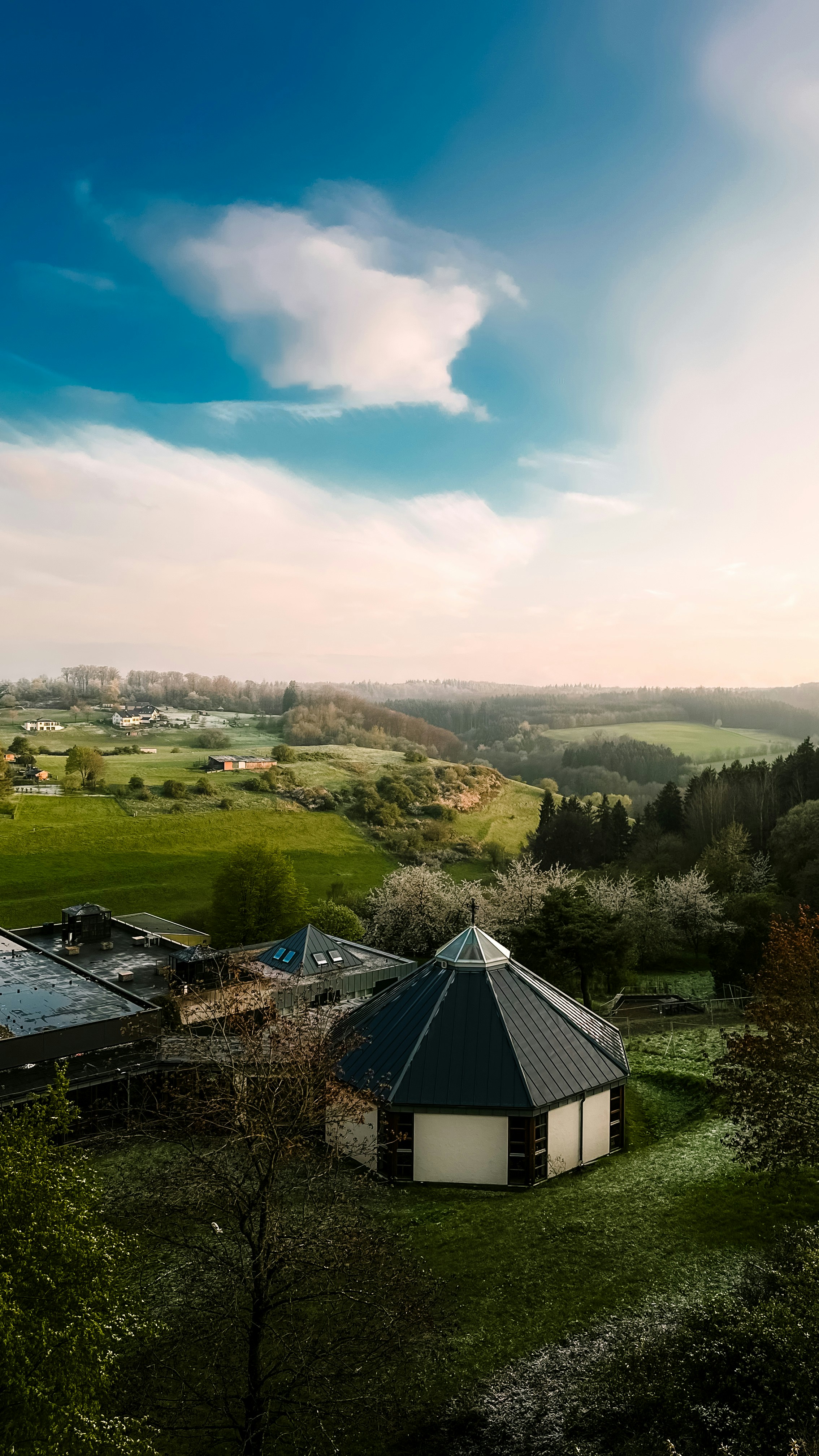Sunlit Village Crest: A Blue-Tiled Roof Amid Rolling Fields