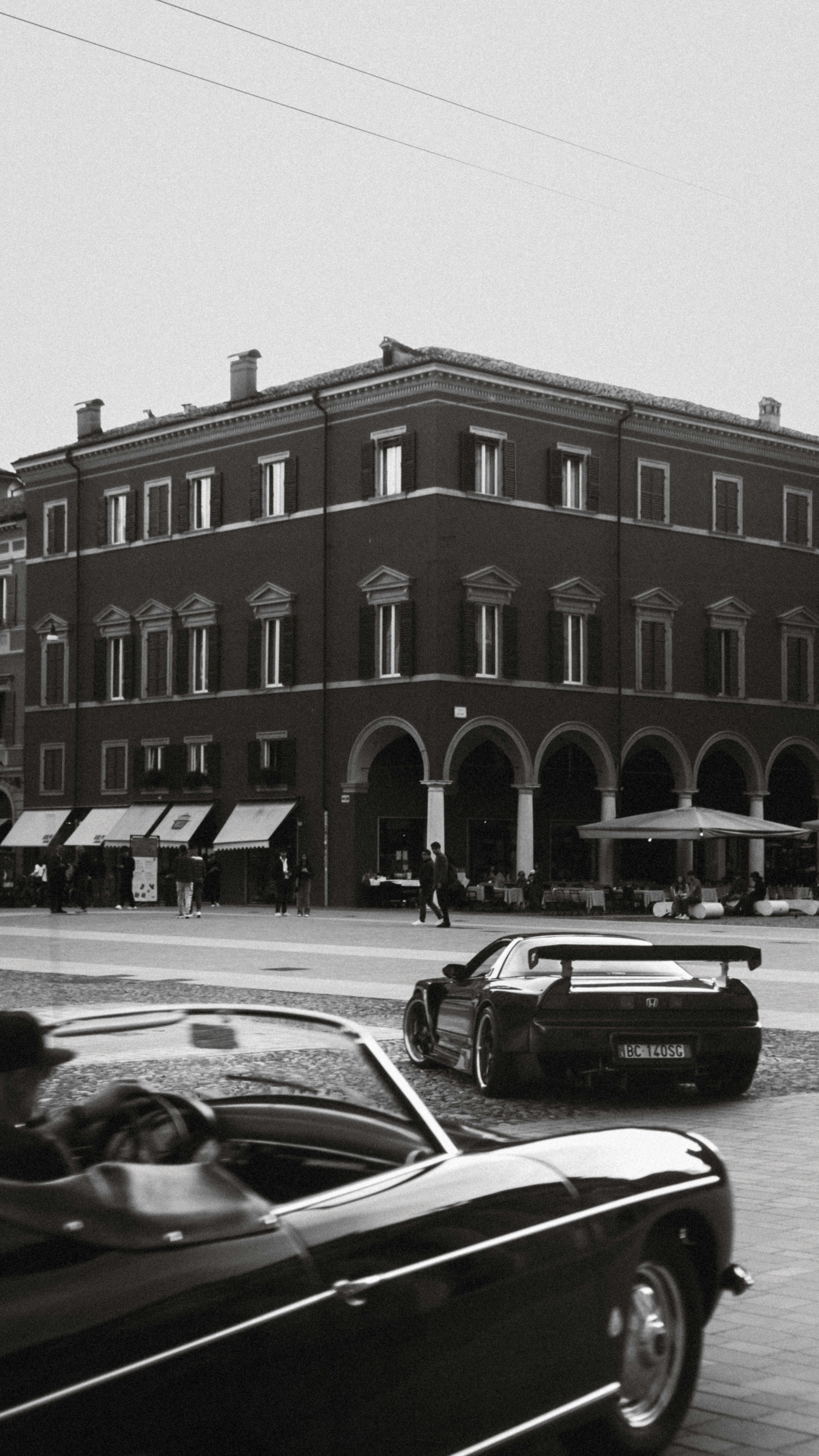Monochrome Piazza: Arched Facade, Café, and Vintage Cars