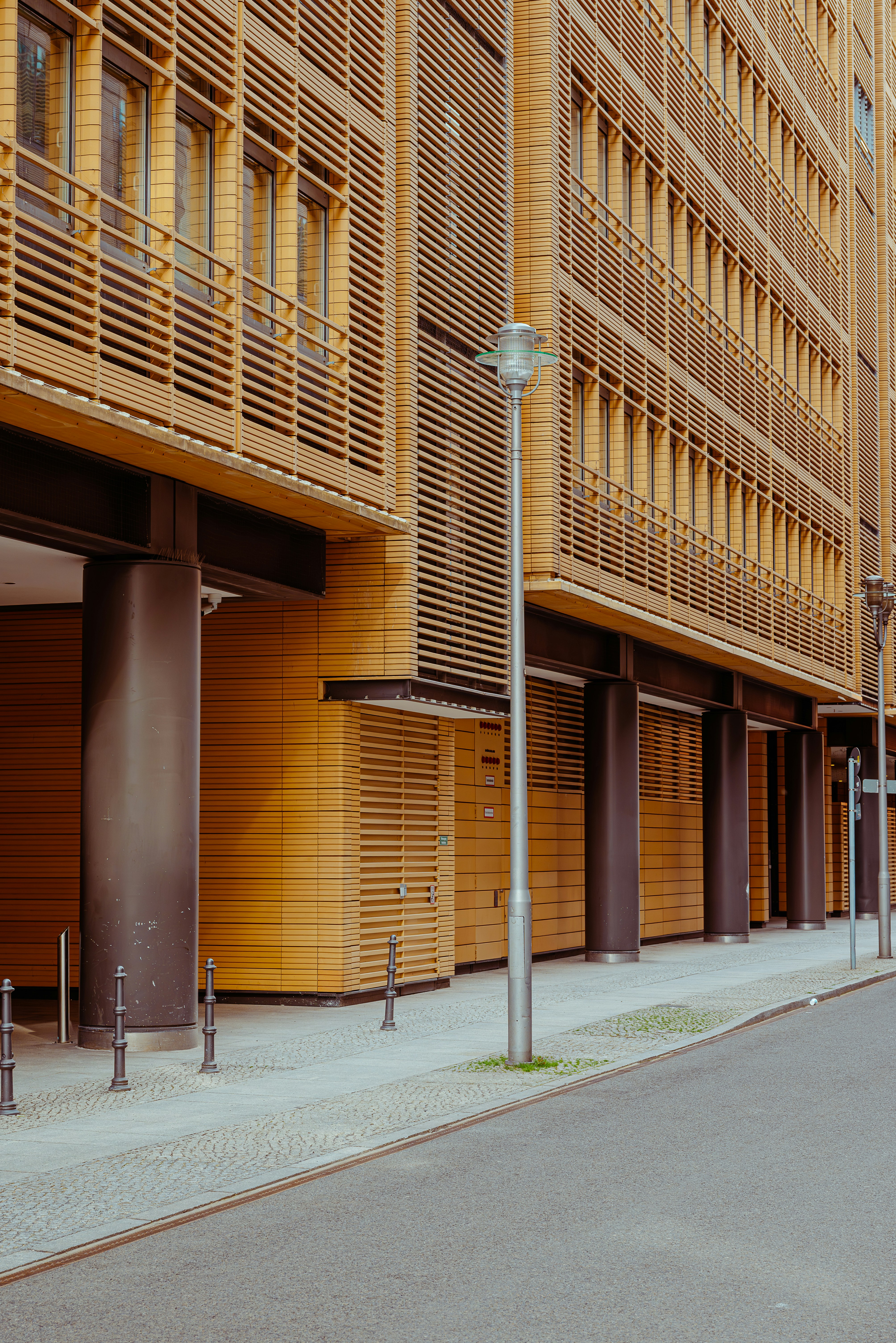 A photograph of an urban street lined with ribbed amber façades. A solitary streetlamp rises between columns, adding contrast and depth.