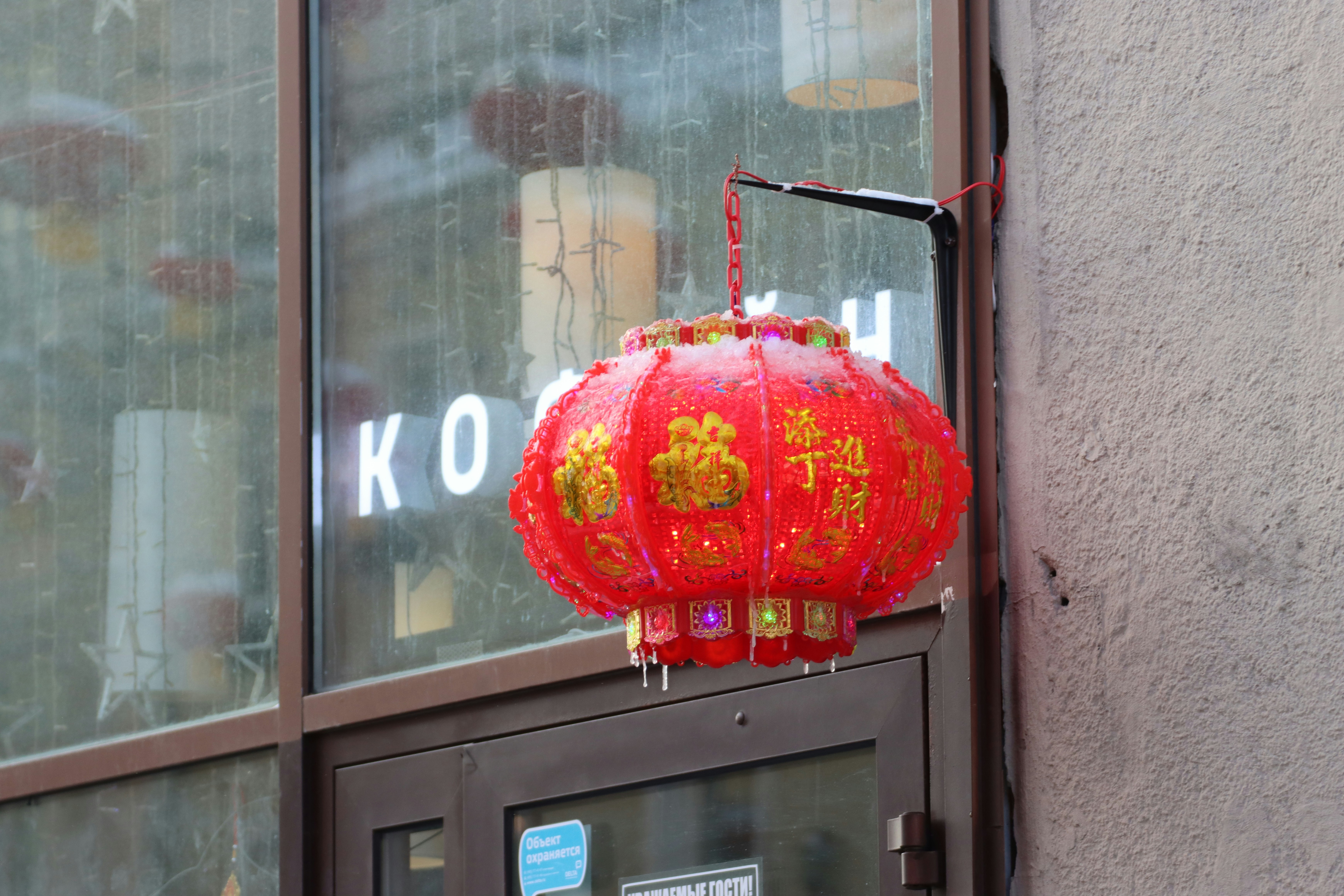 Red Lantern Adorned by Golden Charms Above a Glass Door