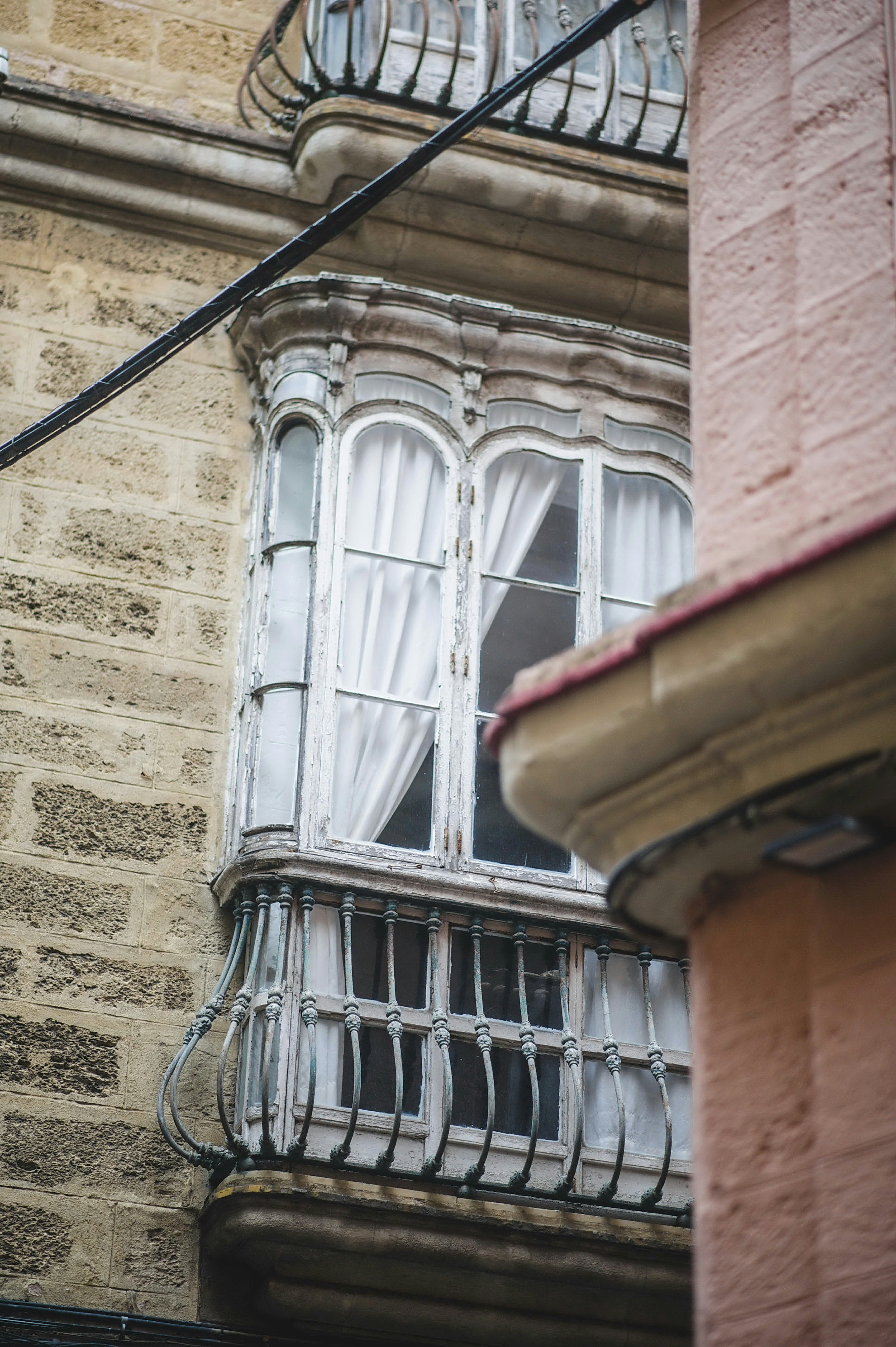Timeworn Bay Window: Ironwork and Draped Light on a Stone Facade