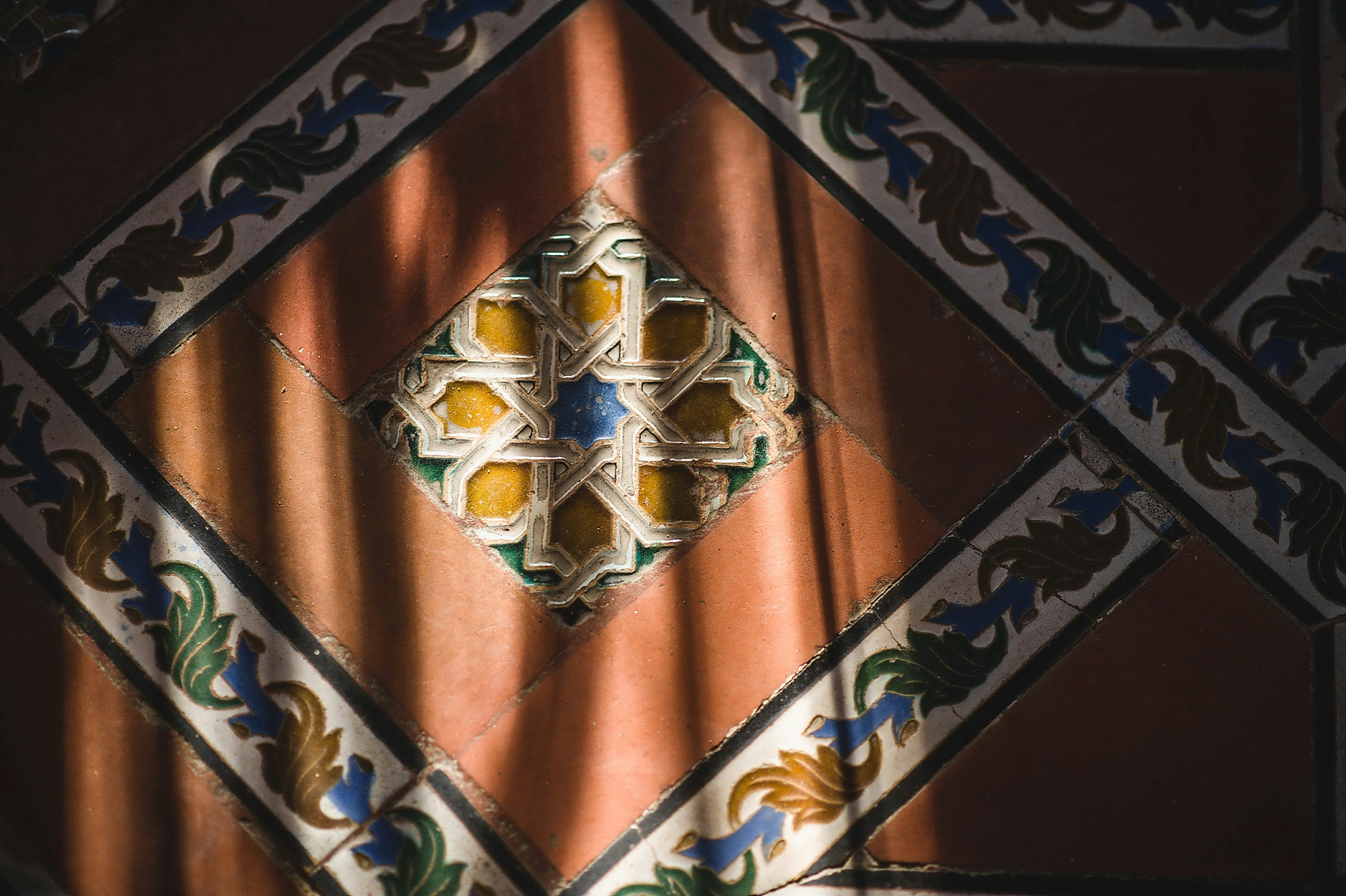 Decorative tile floor with a central diamond medallion and colorful borders, illuminated by diagonal sunlight.