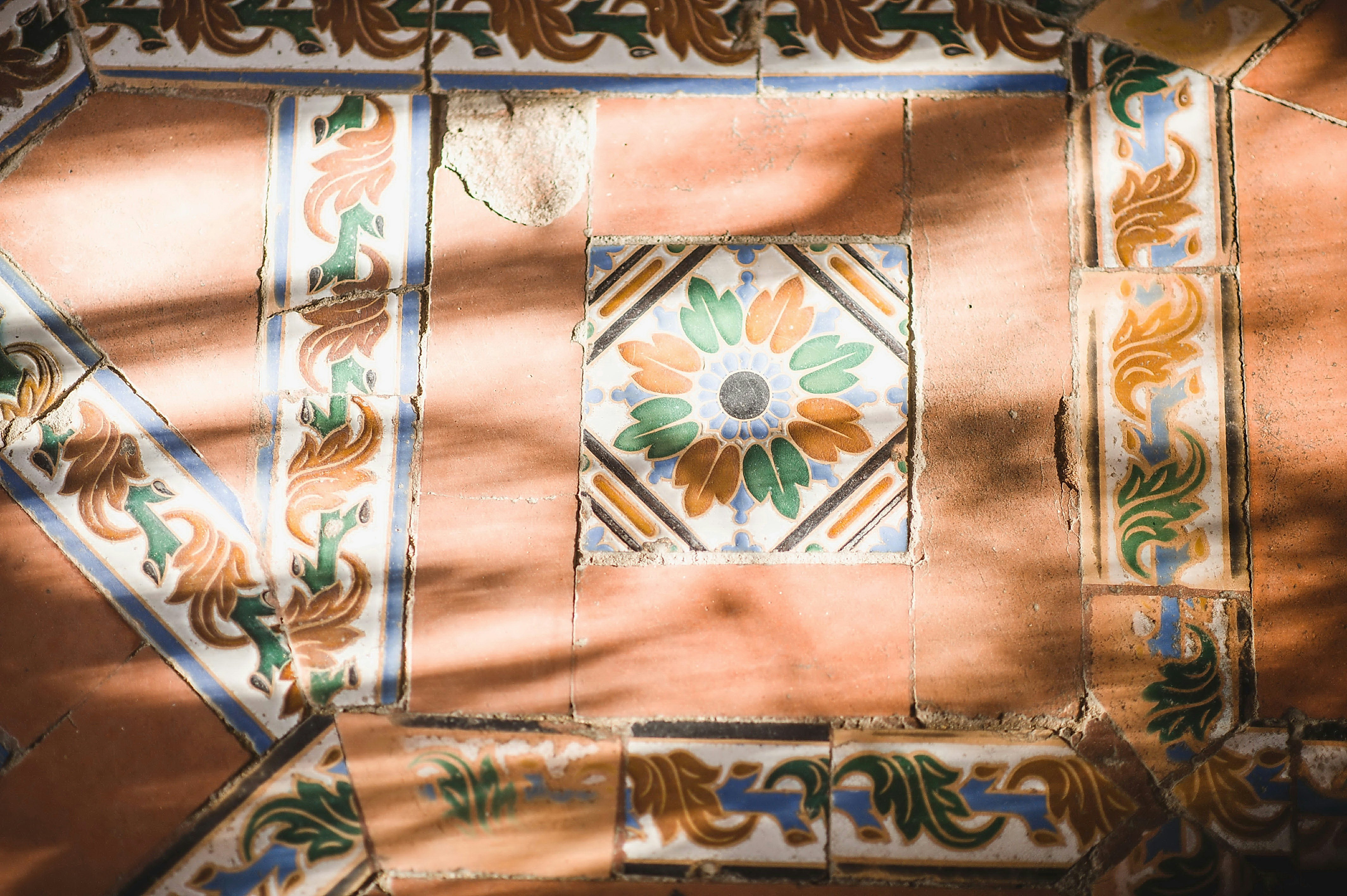 Ornate ceramic tiles with floral and geometric patterns cast in dappled sunlight.