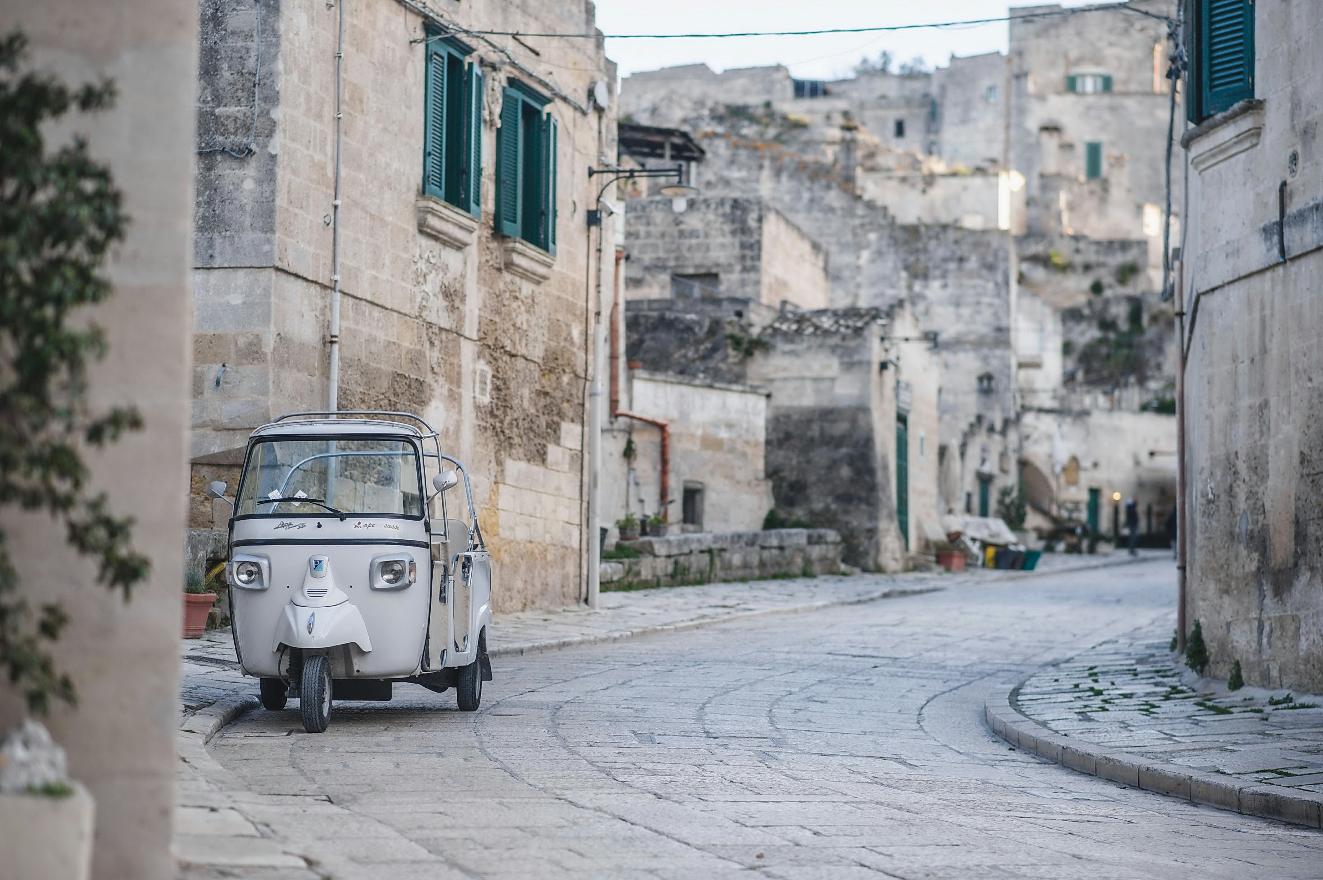 White Vintage Three-Wheeled Scooter on a Curved Mediterranean Cobblestone Street