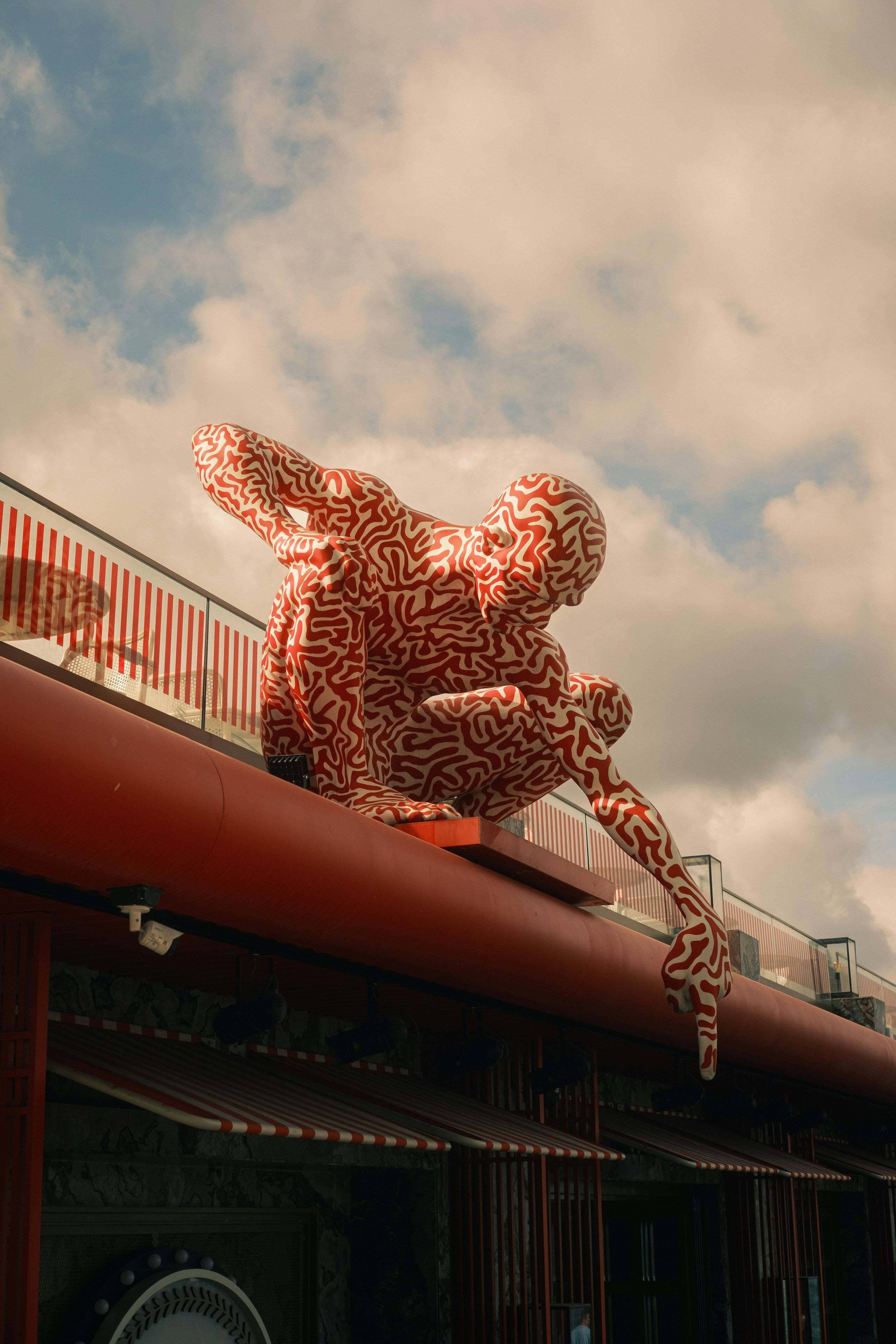 Giant Red-Patterned Figure Reclining Above a Rooftop Balcony