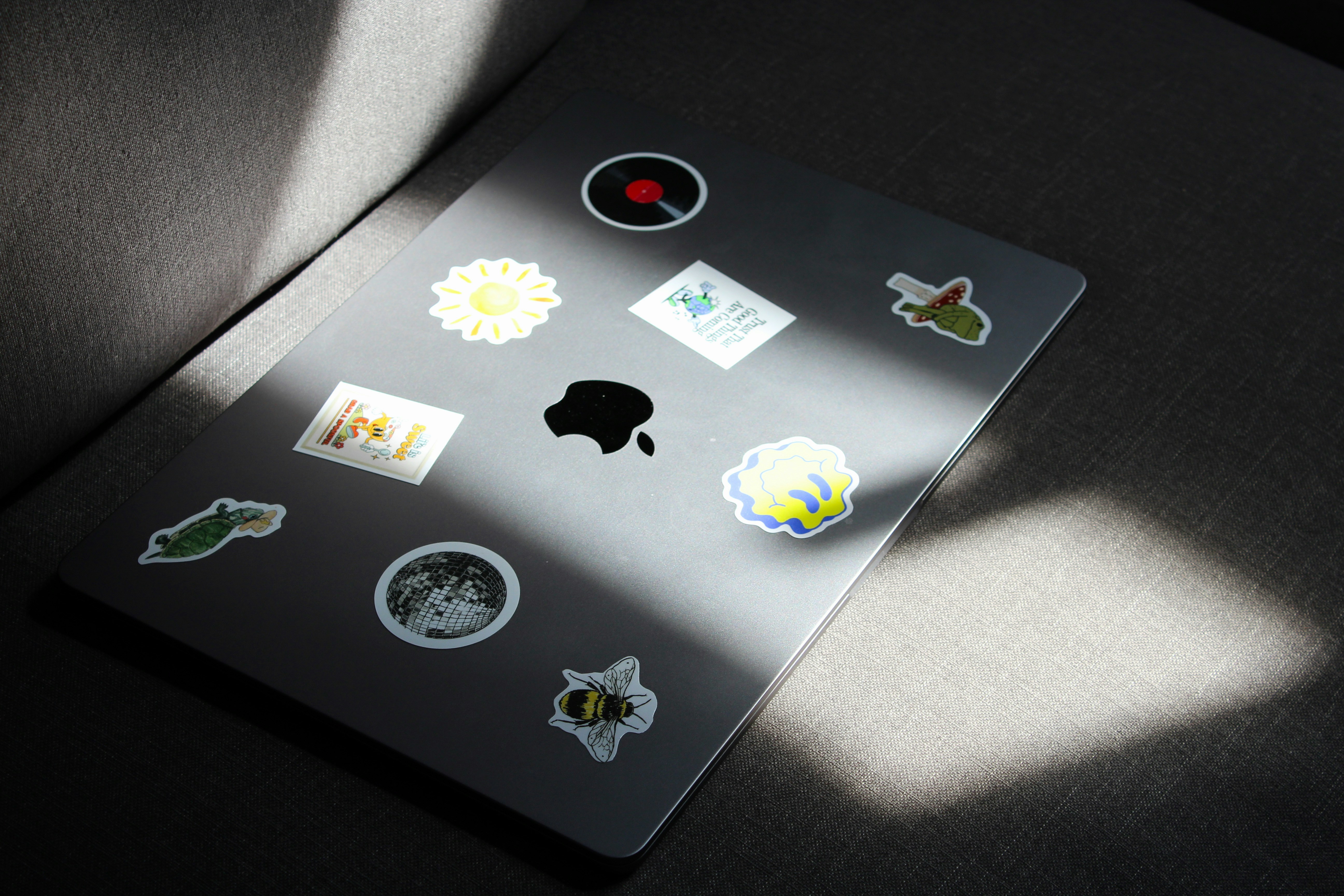 Apple laptop on a grey couch in the sun with stickers on it