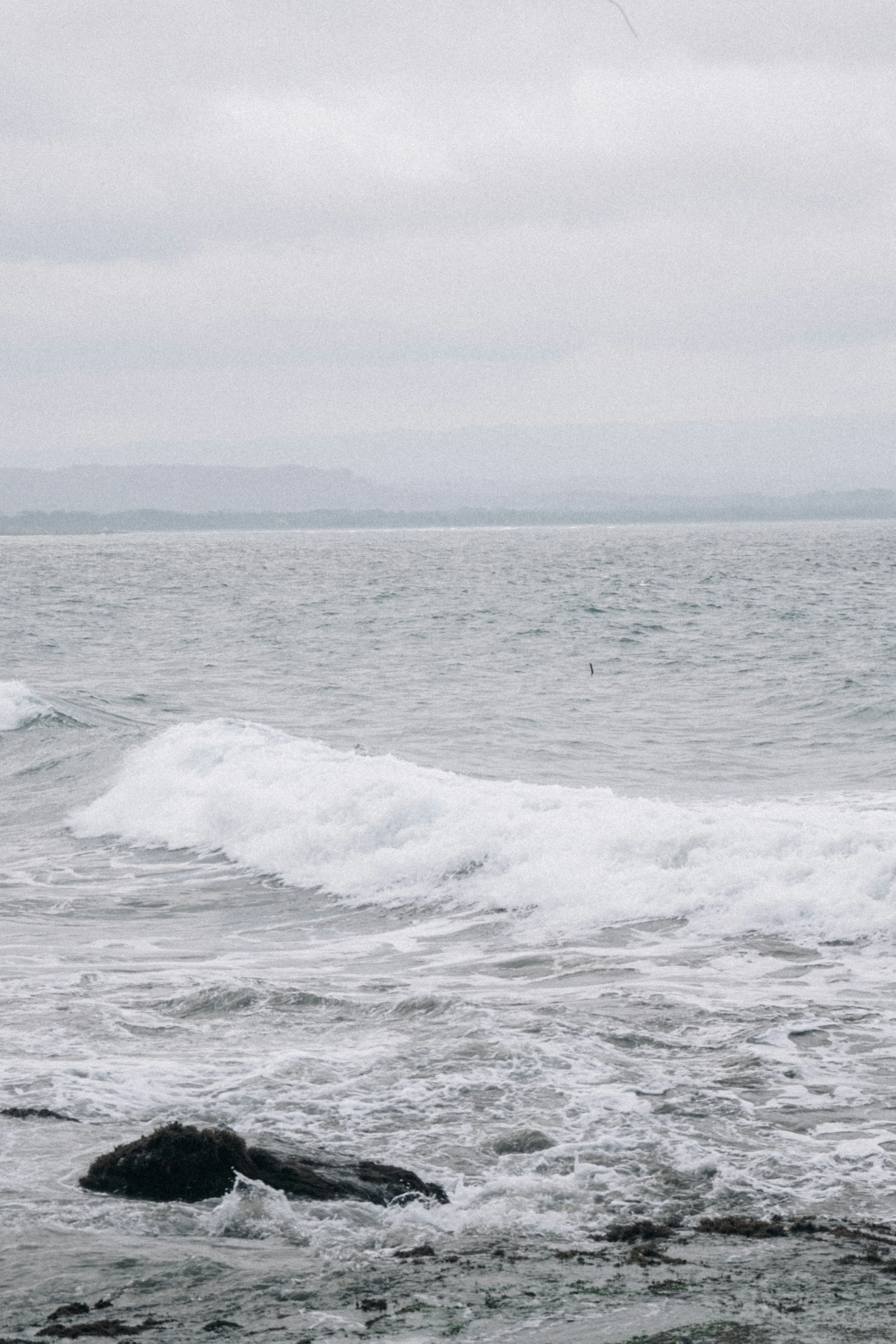 Gentle waves caressing rocky shoreline under a cloudy sky, evoking a serene coastal atmosphere.
