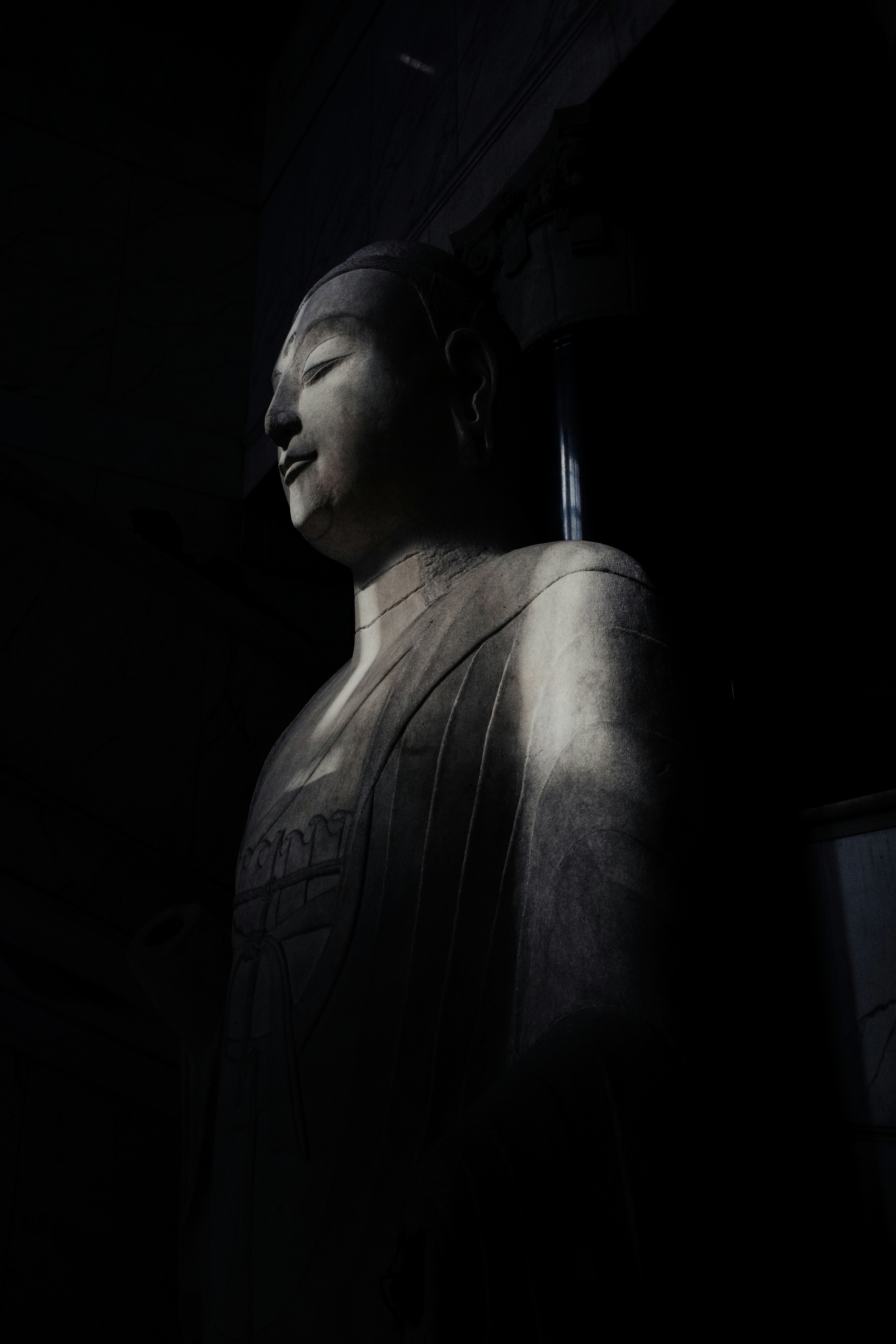A serene statue of a figure draped in flowing robes, partially illuminated by soft light in a dimly lit space.