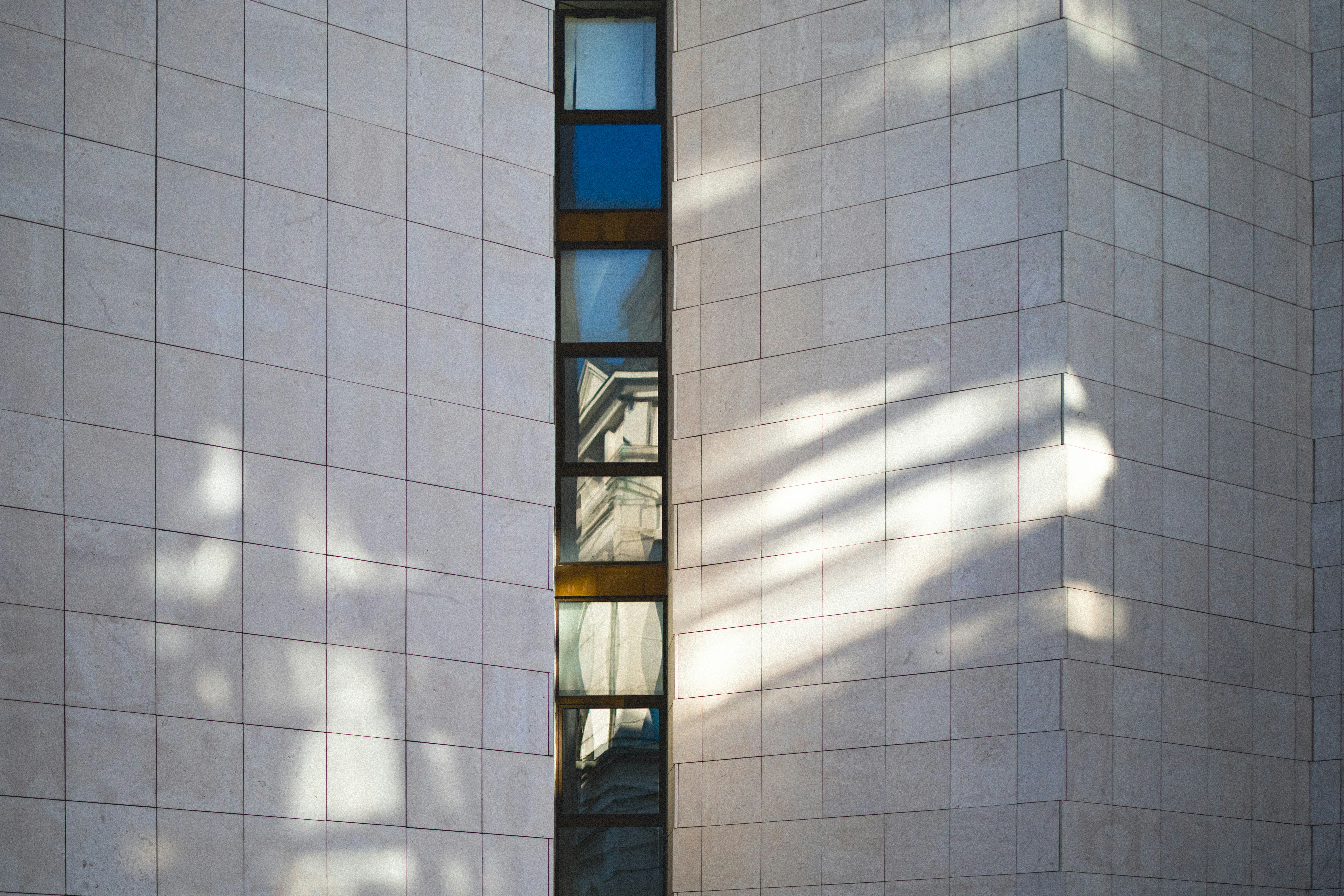 Tall window framed by geometric shadows on a textured wall facade.