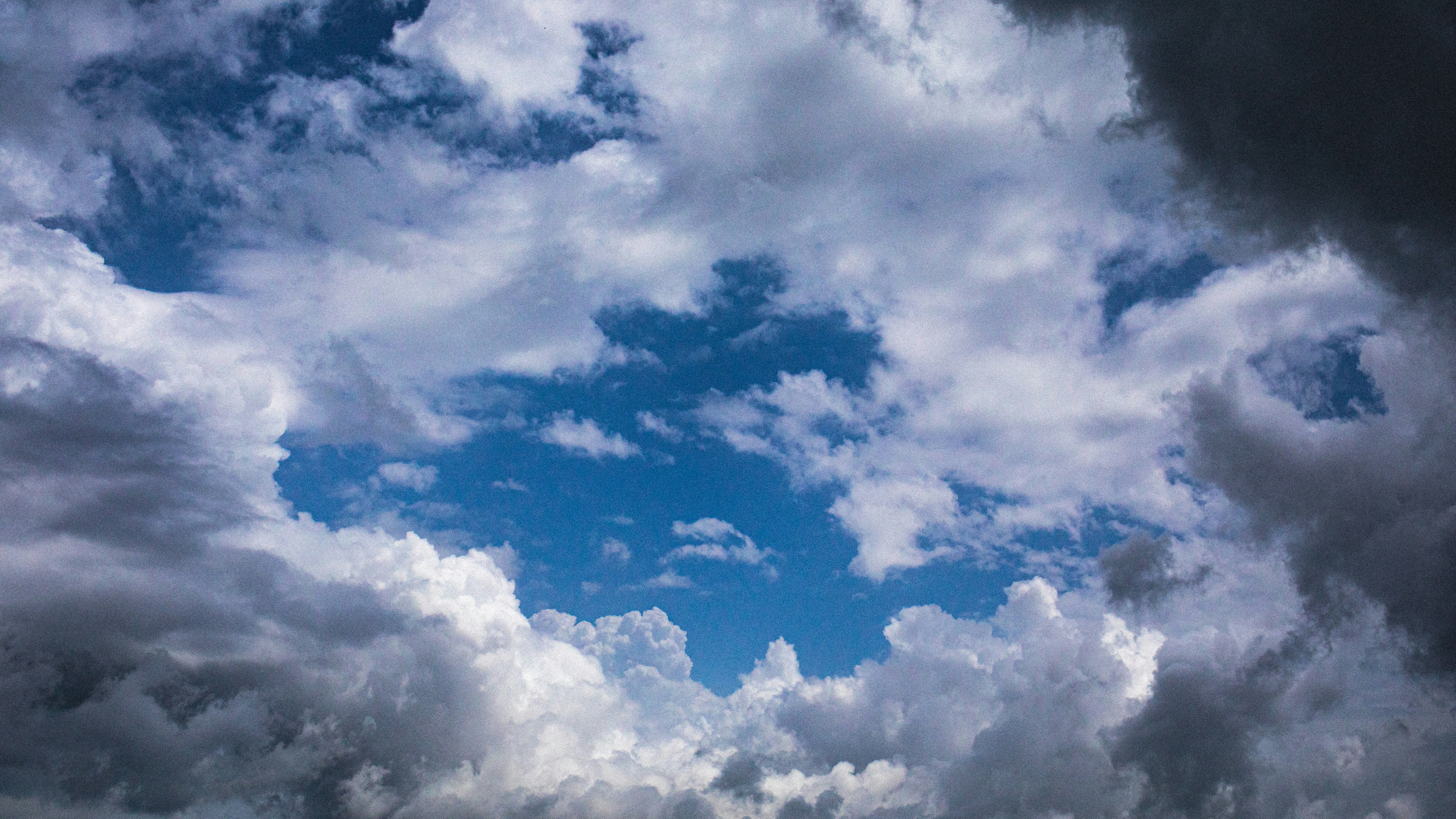 A dynamic sky filled with swirling clouds, revealing patches of blue amidst the gray. The interplay of light and shadow creates a dramatic atmosphere.
