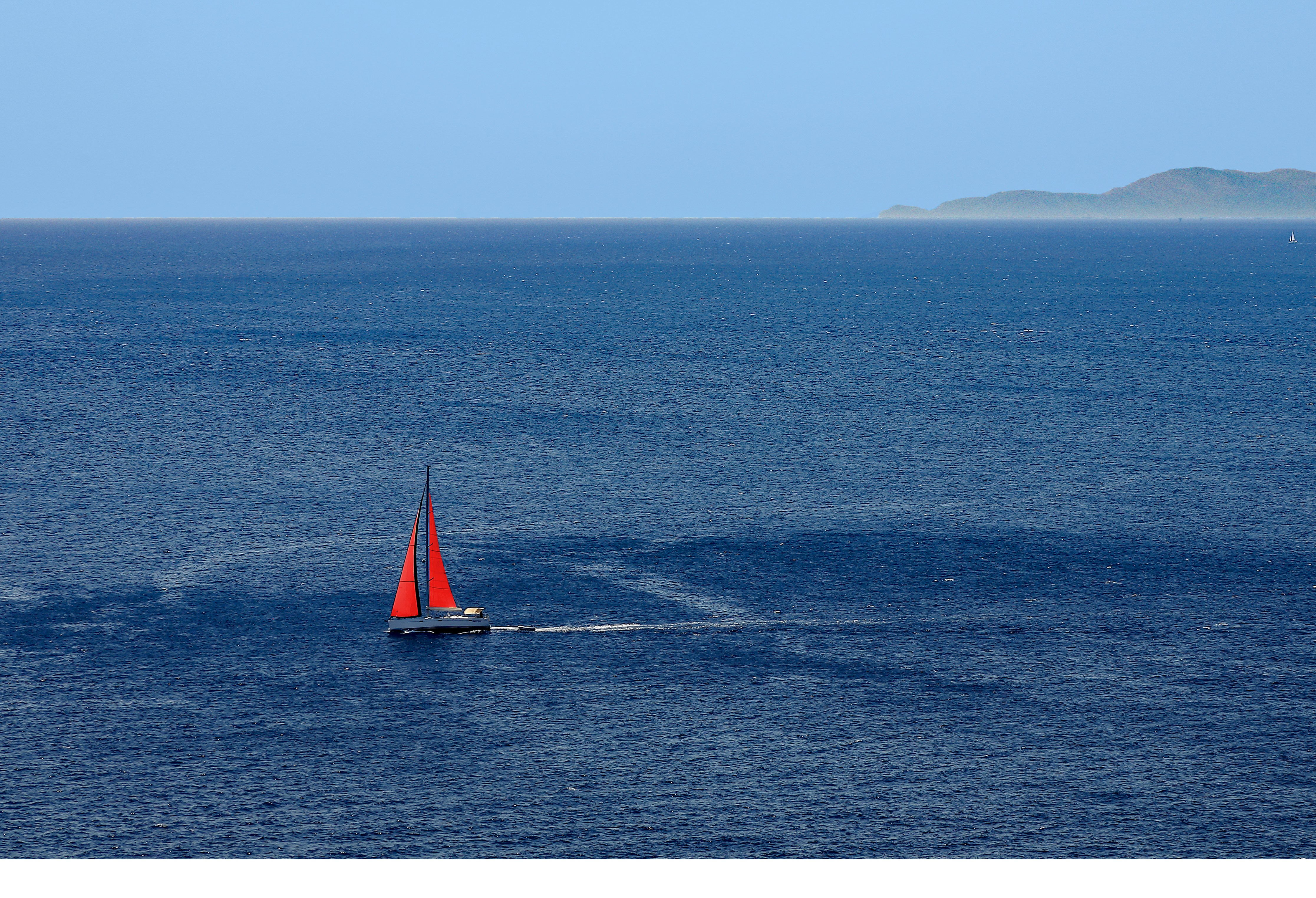 Red-sailed Vessel Traces a Quiet Wake Across Open Blue