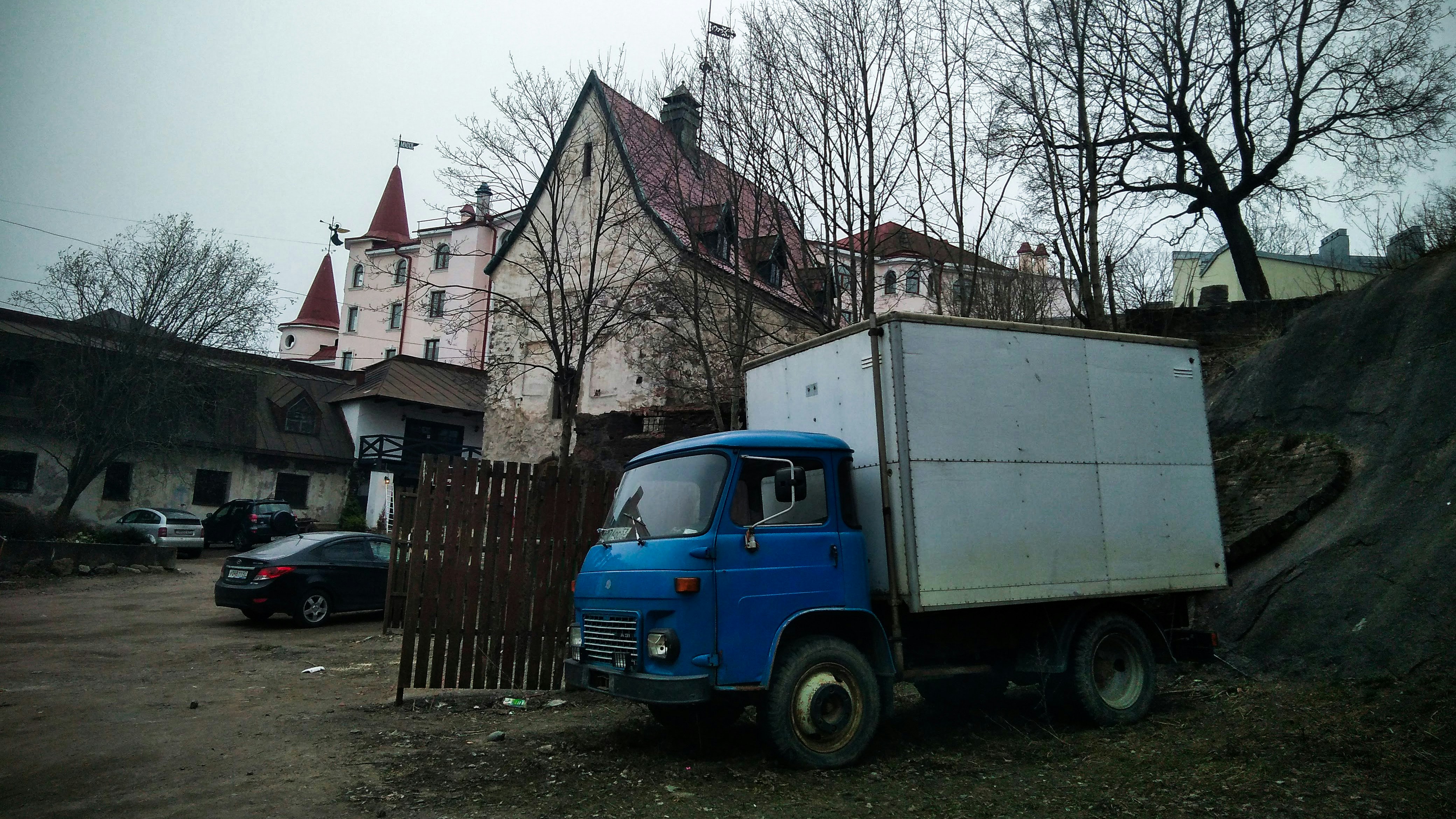 Blue Freight Truck in a Weathered Yard Beneath Bare Trees