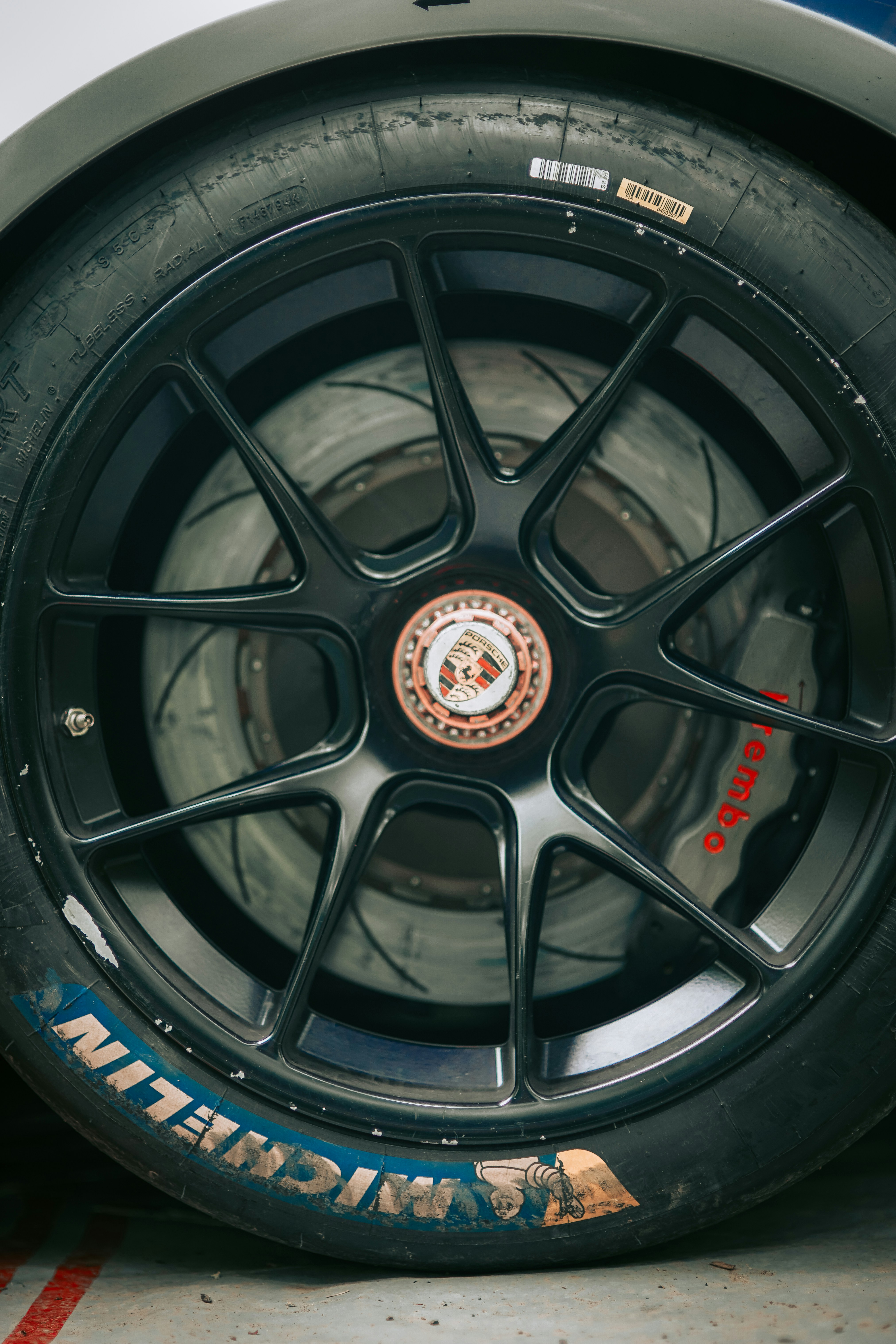 Center Hub in Focus: Porsche Crest Behind a Black Alloy Wheel with Brembo Red Caliper and Michelin Tire