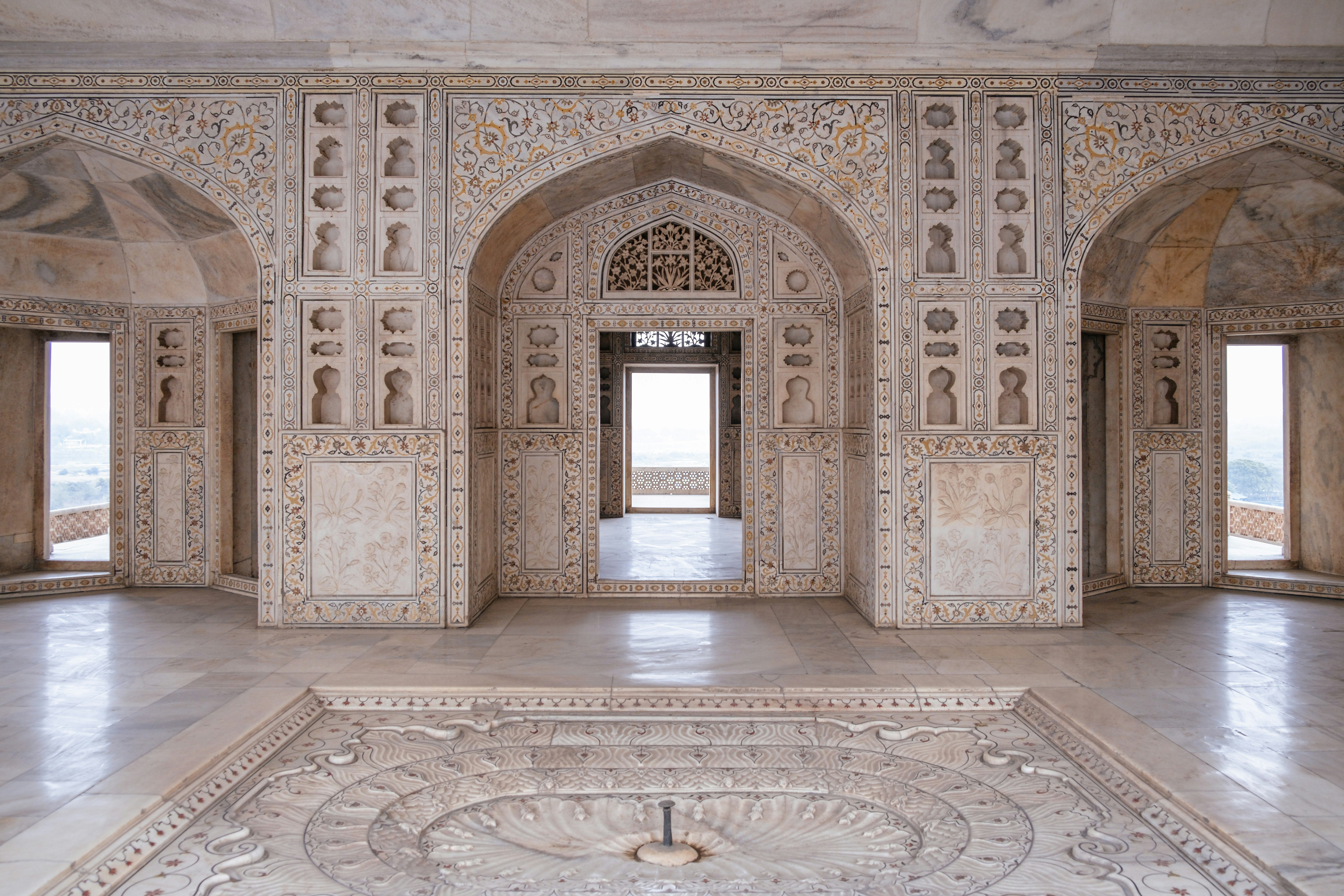 Intricate stone carvings and arches frame a serene interior space, leading to an expansive view beyond. The ornate details reflect a rich architectural heritage.