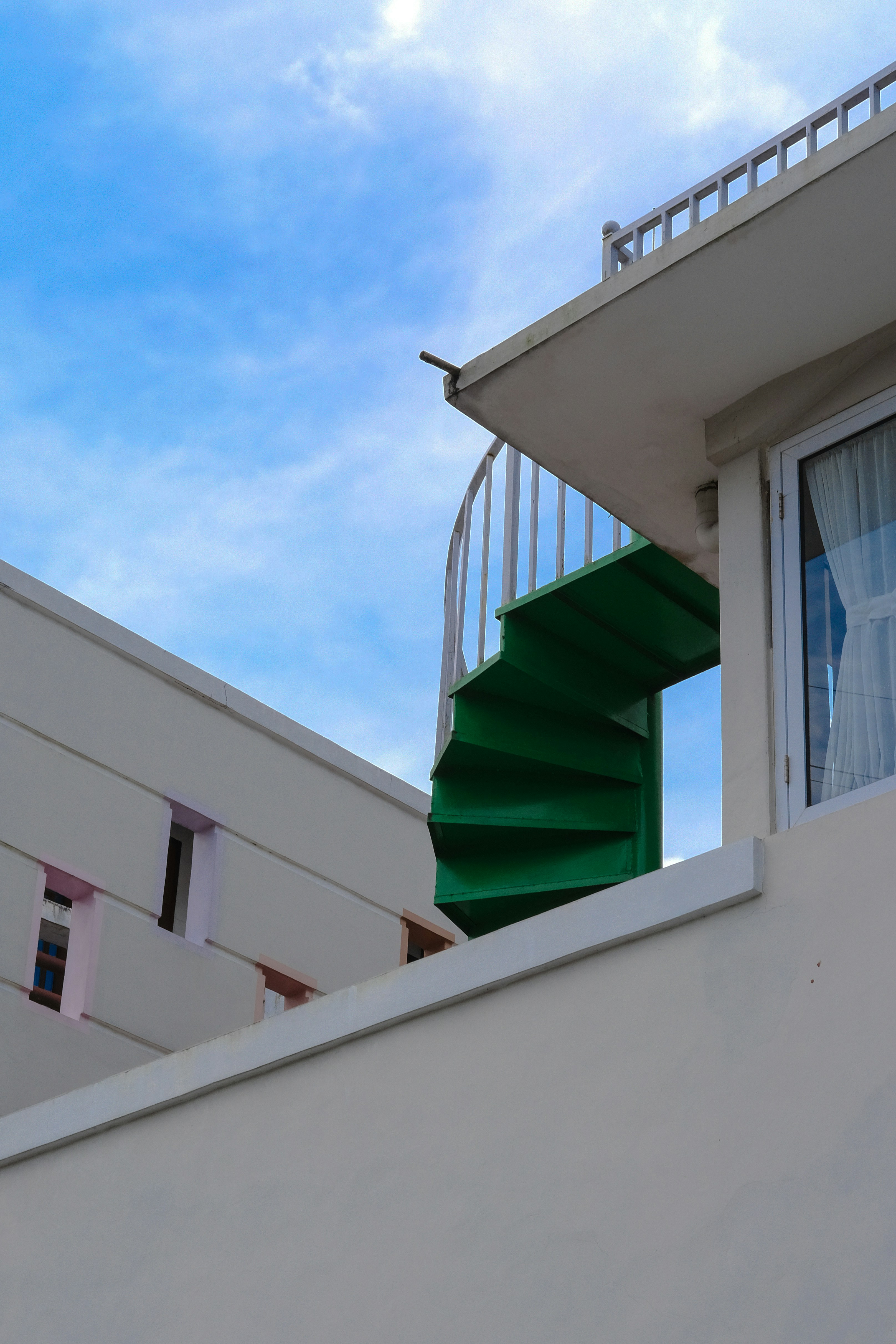 Emerald Spiral Staircase Rising Along a White Terrace Under a Bright Sky