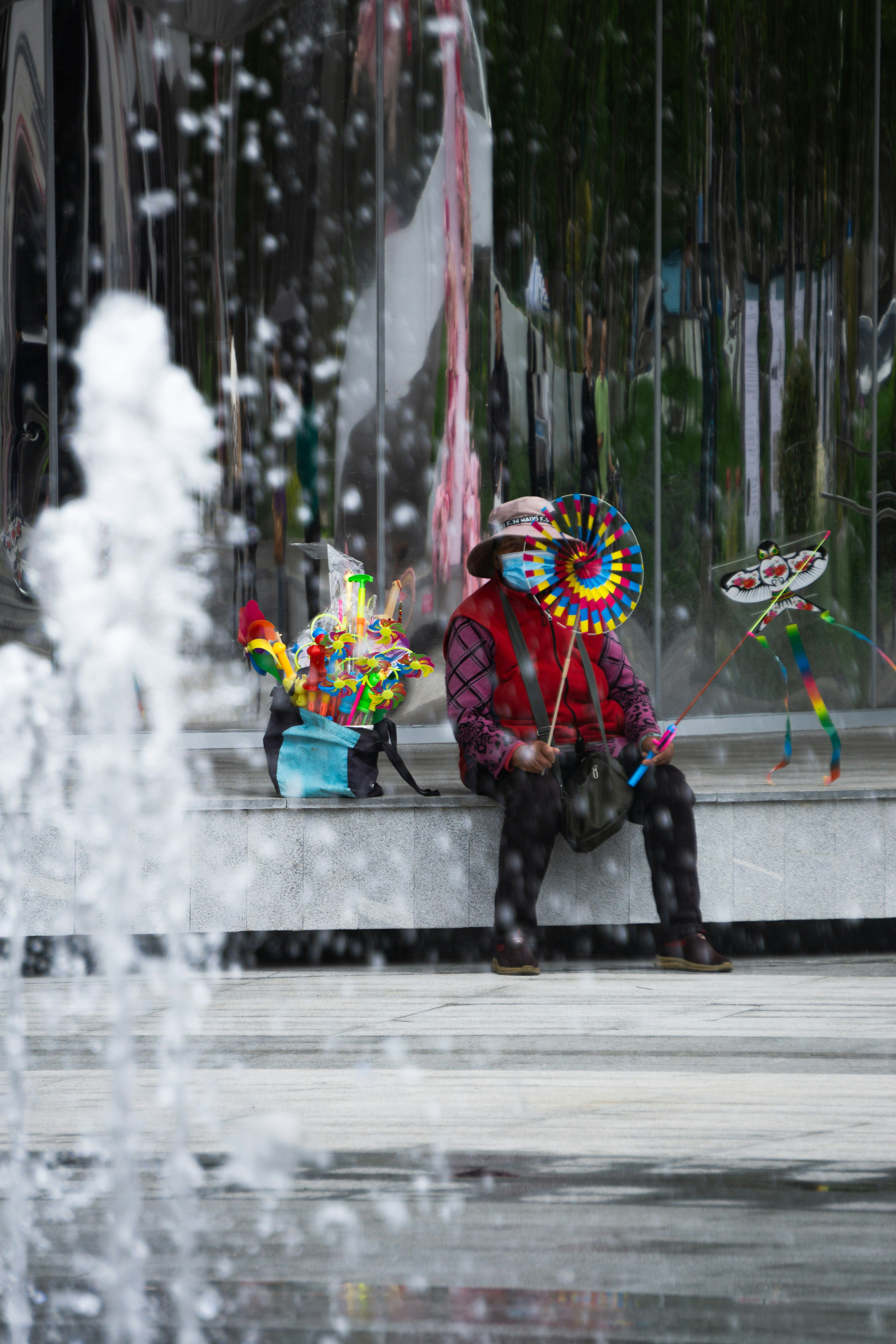 Colorful Carousel: A Street Vendor with Wind-Driven Pinwheels by a Glass Wall