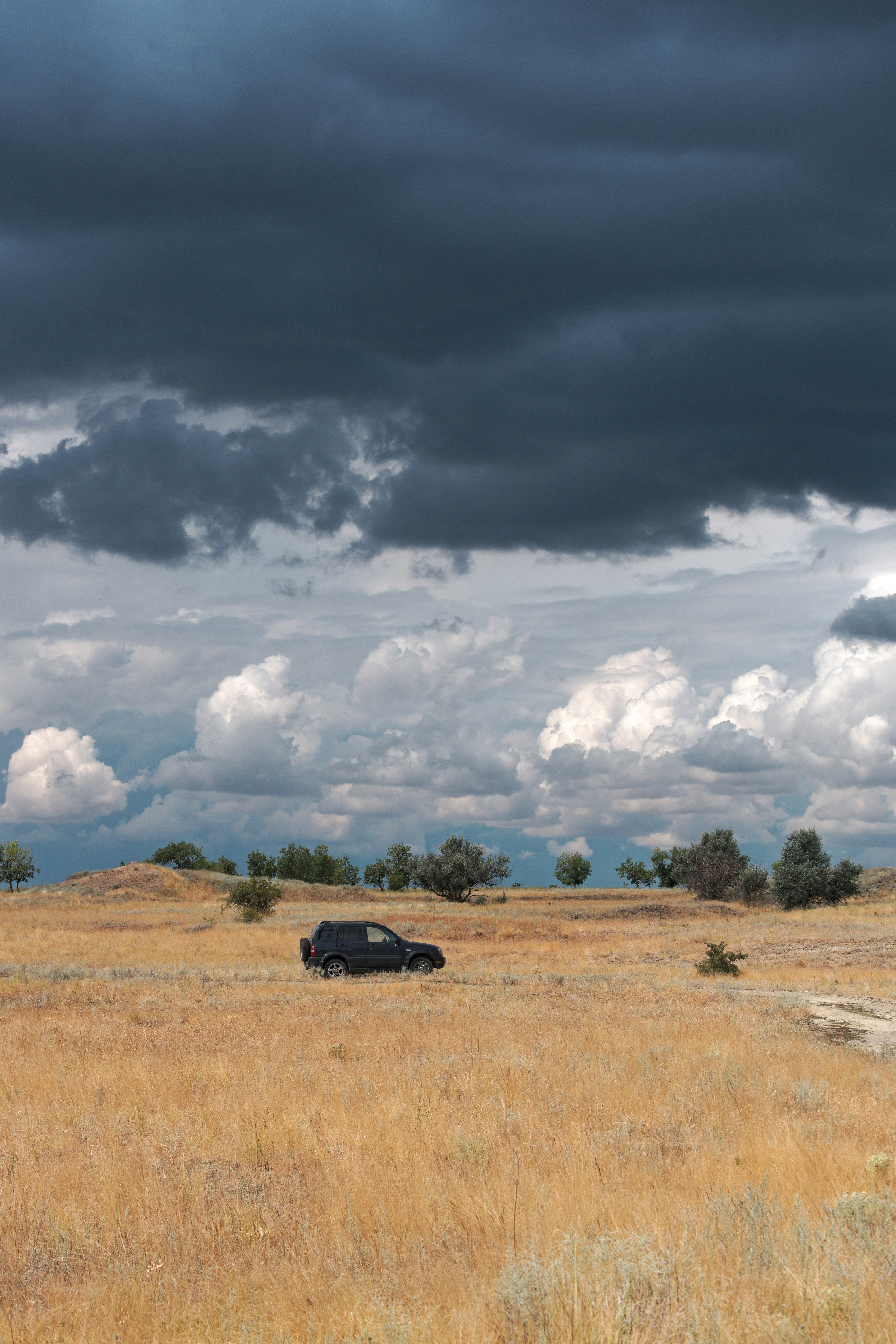 Lone SUV on a sunlit prairie as storm clouds roll in