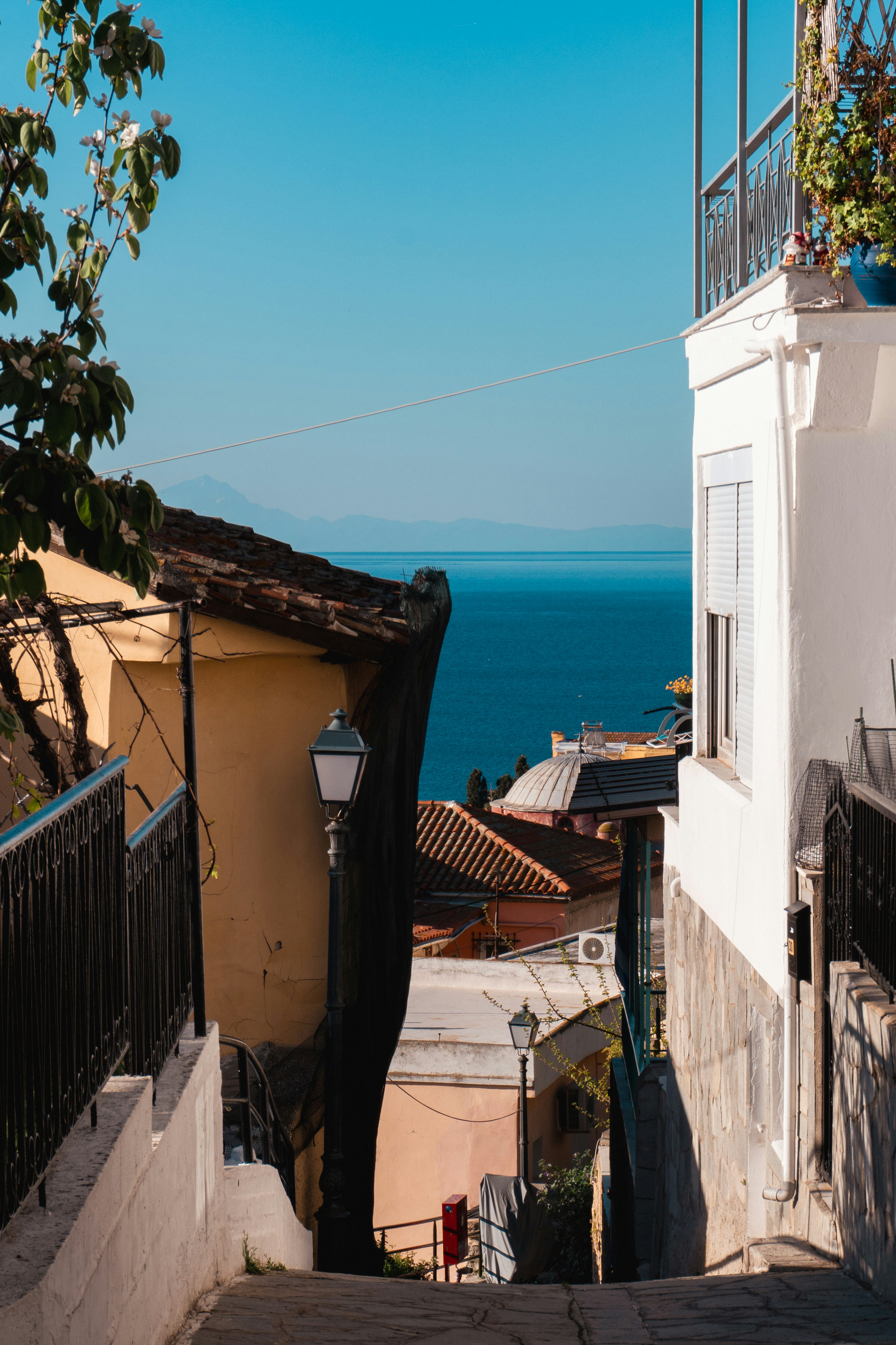 Charming narrow street leading down to a tranquil seaside view, framed by vibrant buildings and lush greenery.