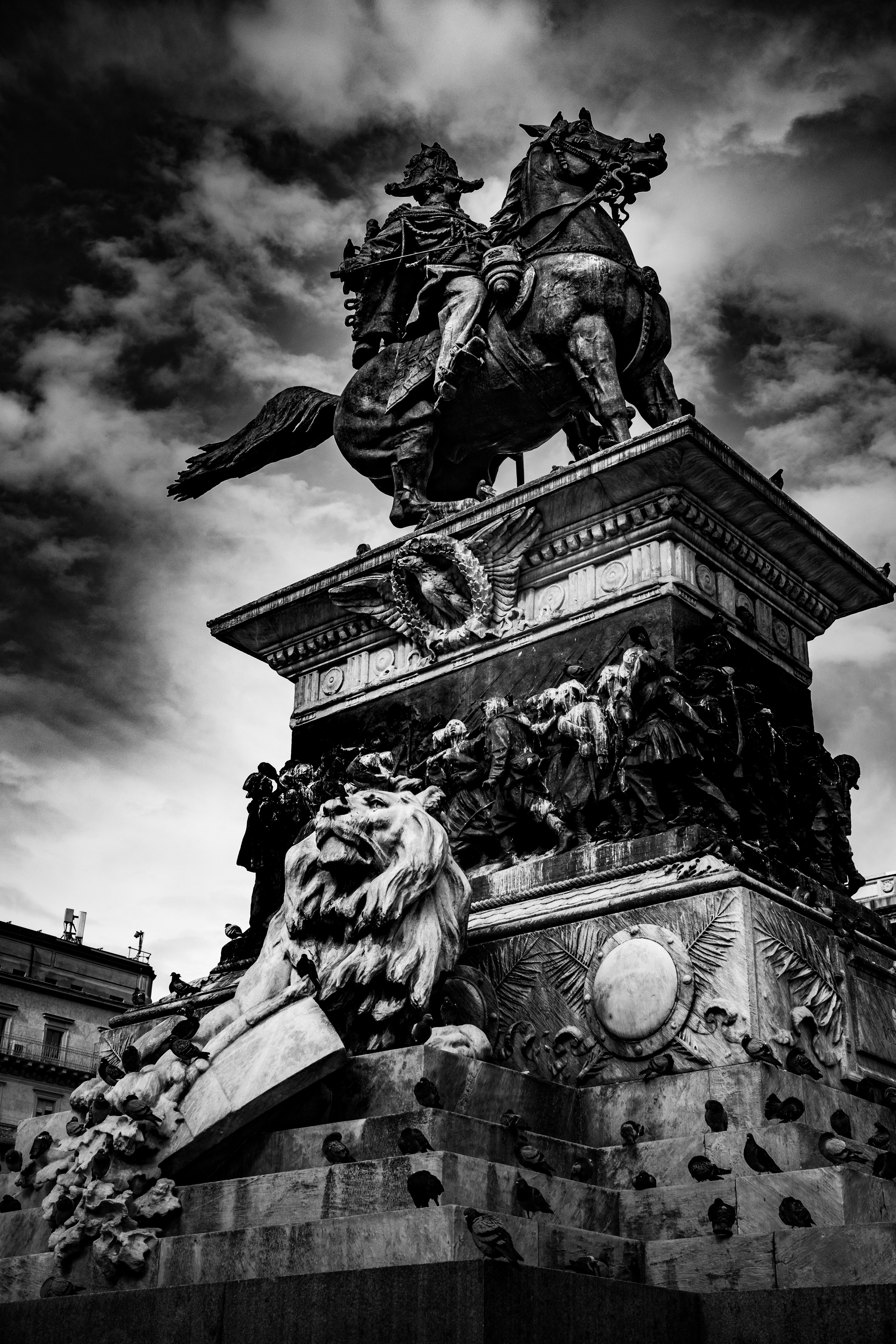 A grand equestrian statue atop a detailed pedestal, featuring a lion and intricate carvings, set against a dramatic sky.