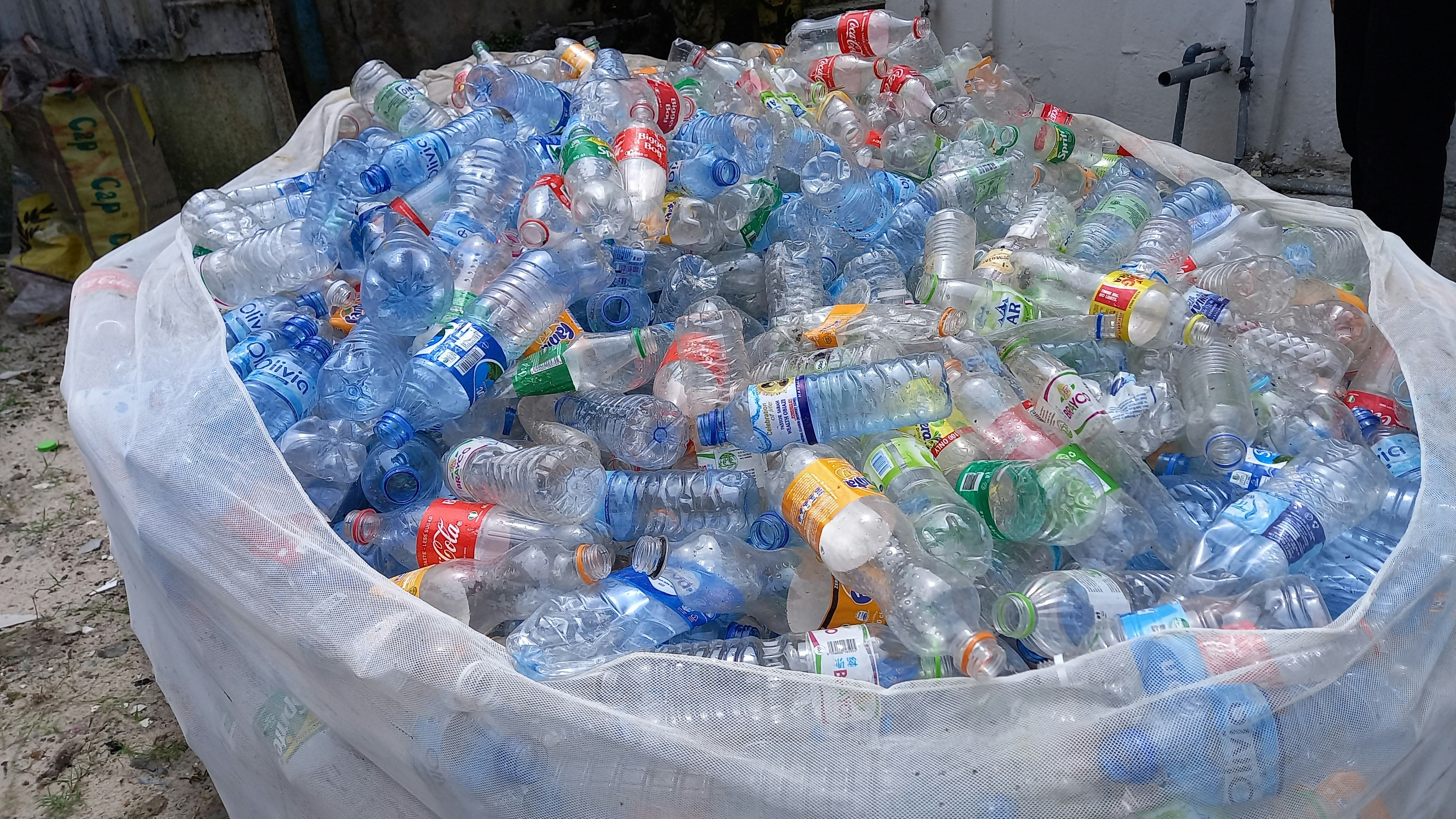 A large collection of plastic bottles piled high in a translucent bag, showcasing the impact of consumer waste. The colors and labels of the bottles create a chaotic yet intriguing visual.