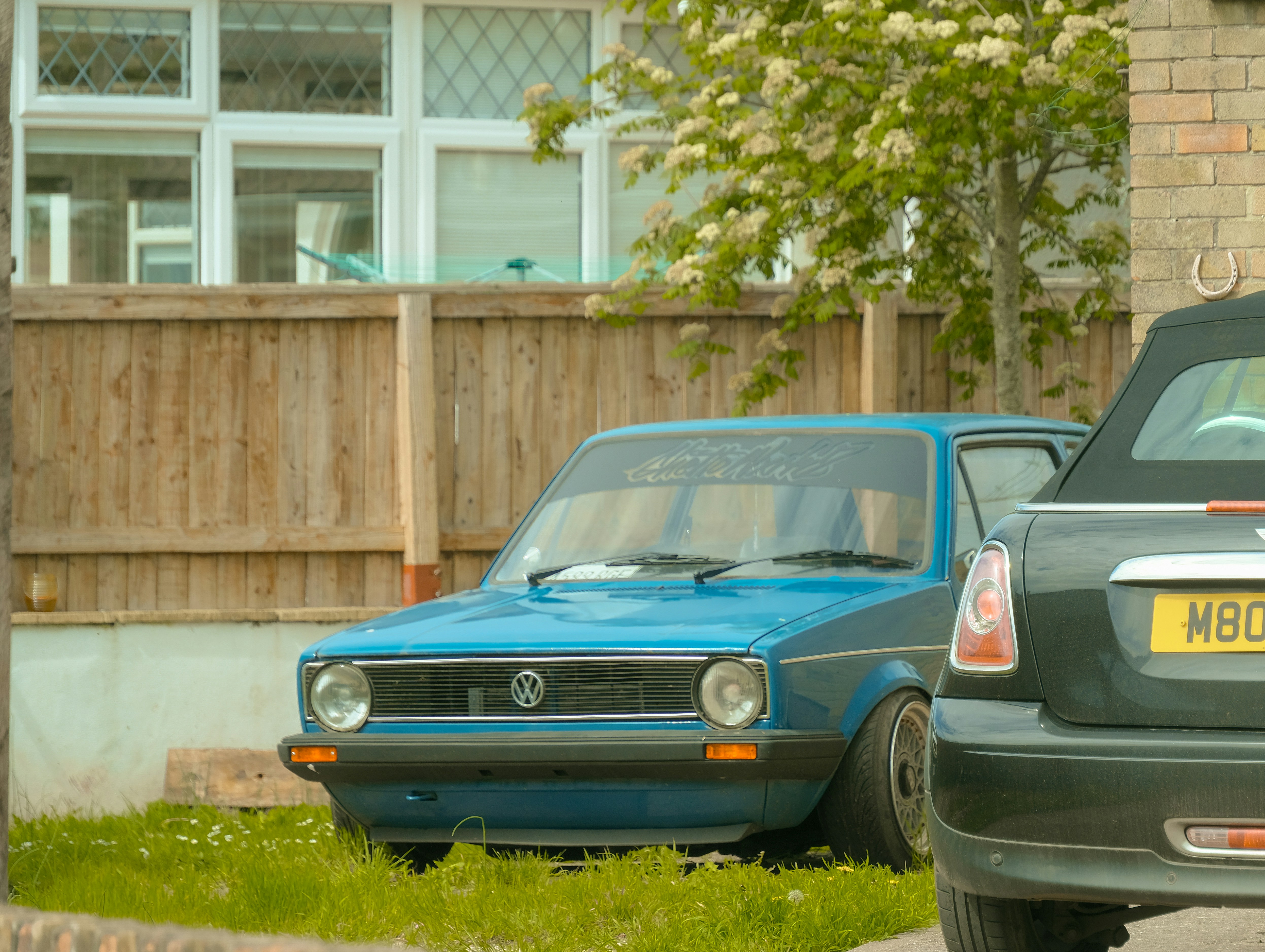Vintage blue car parked beside a modern vehicle in a quiet suburban setting.