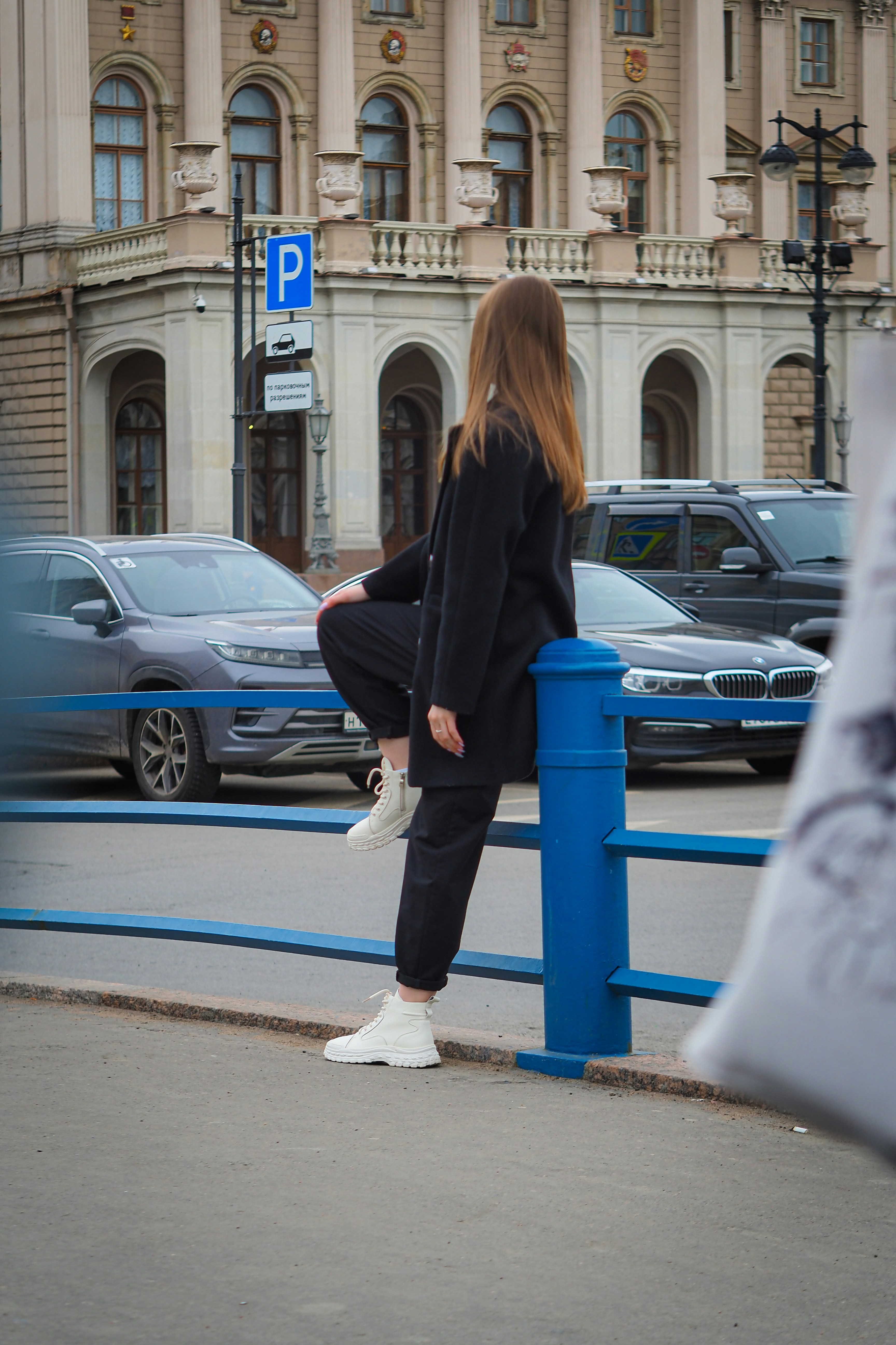 City Edge: A Woman Pauses by the Blue Barrier beside a Grand Facade