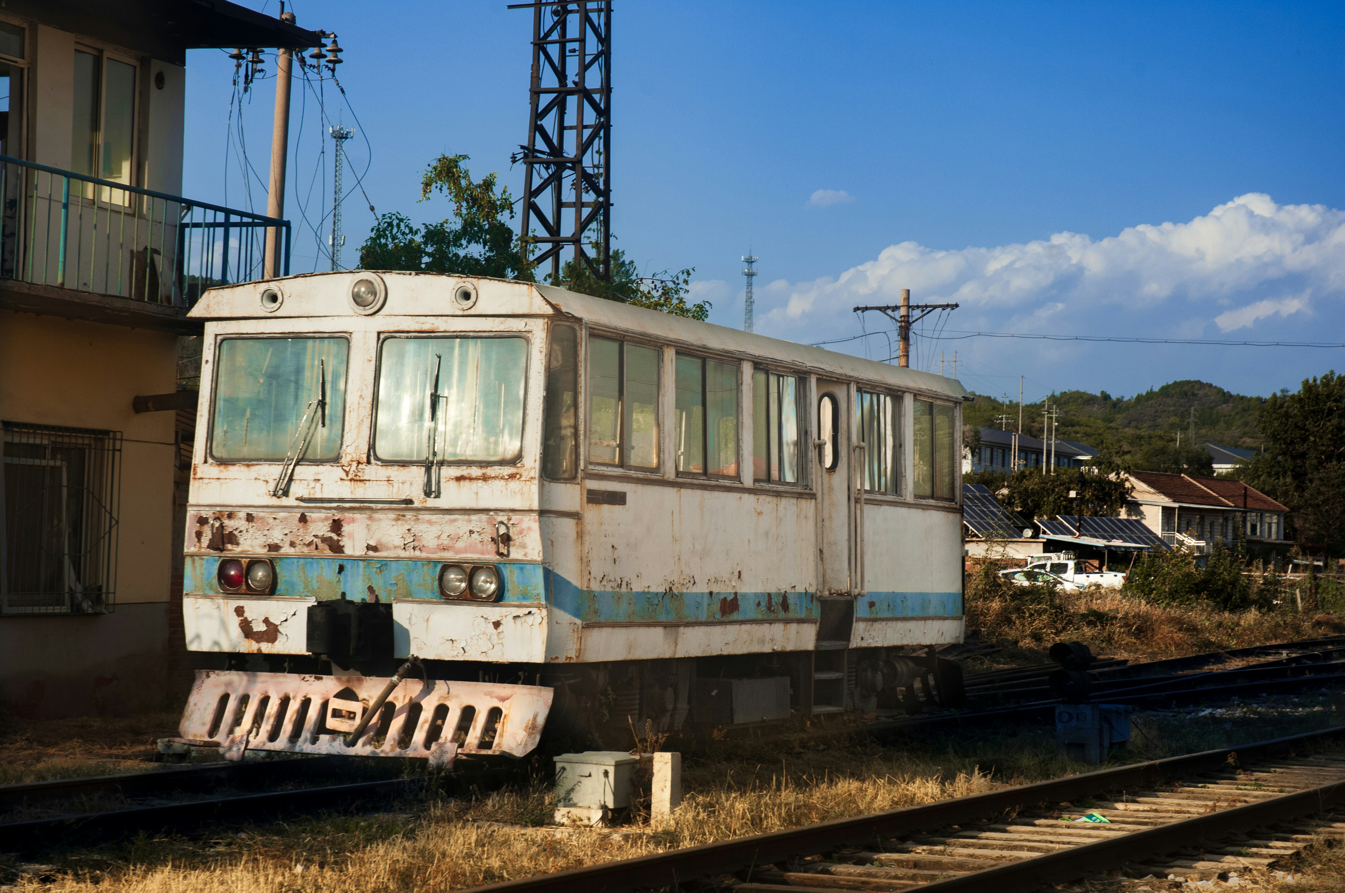 A weathered railcar sits on abandoned tracks beside a small station, with peeling paint and grit revealing years of exposure to the elements.