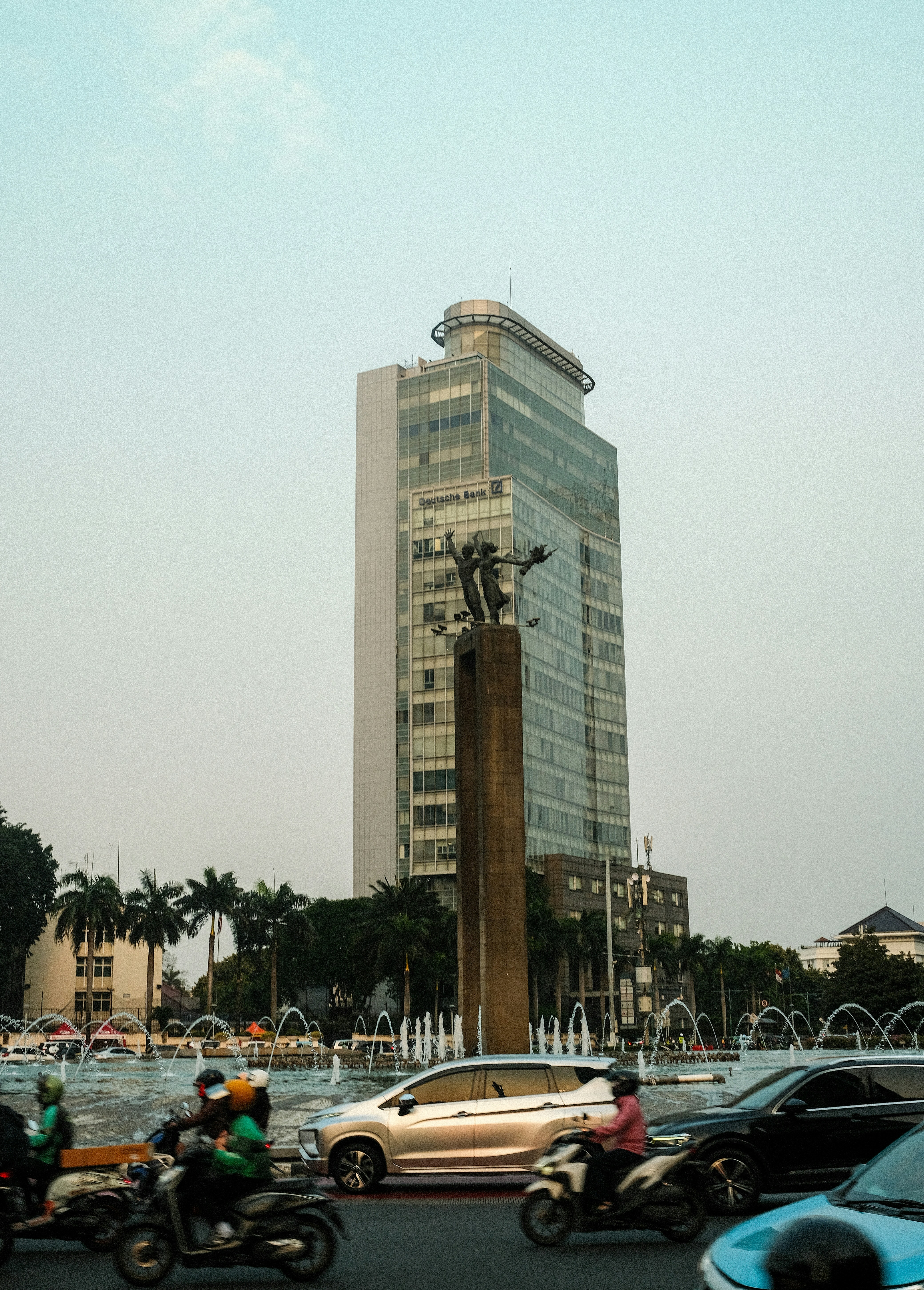 Jakarta street | a group of people riding motorcycles down a street next to a tall building