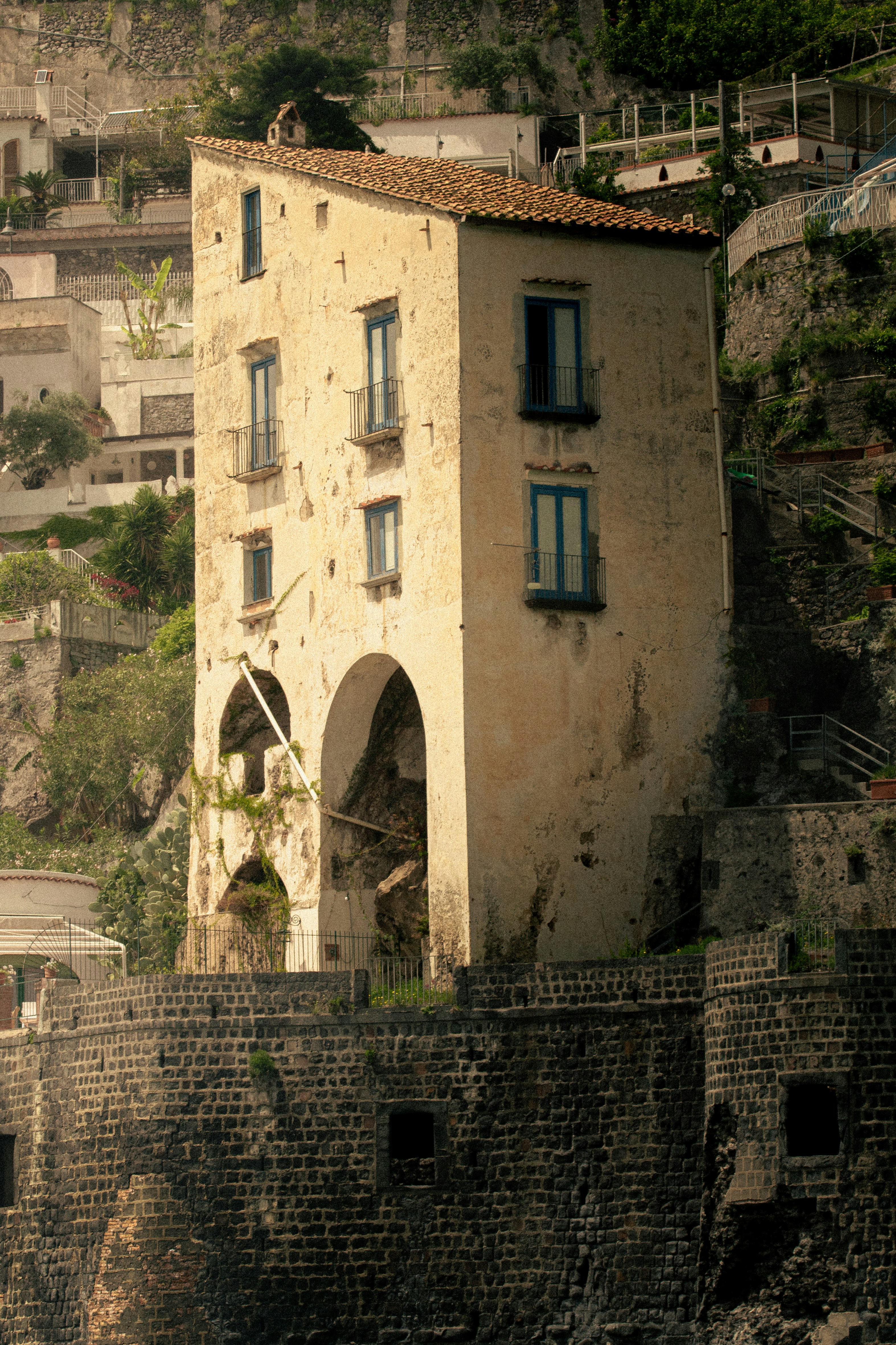 Tall, narrow stone building perched on a rocky hillside with arched entrances and weathered facade.