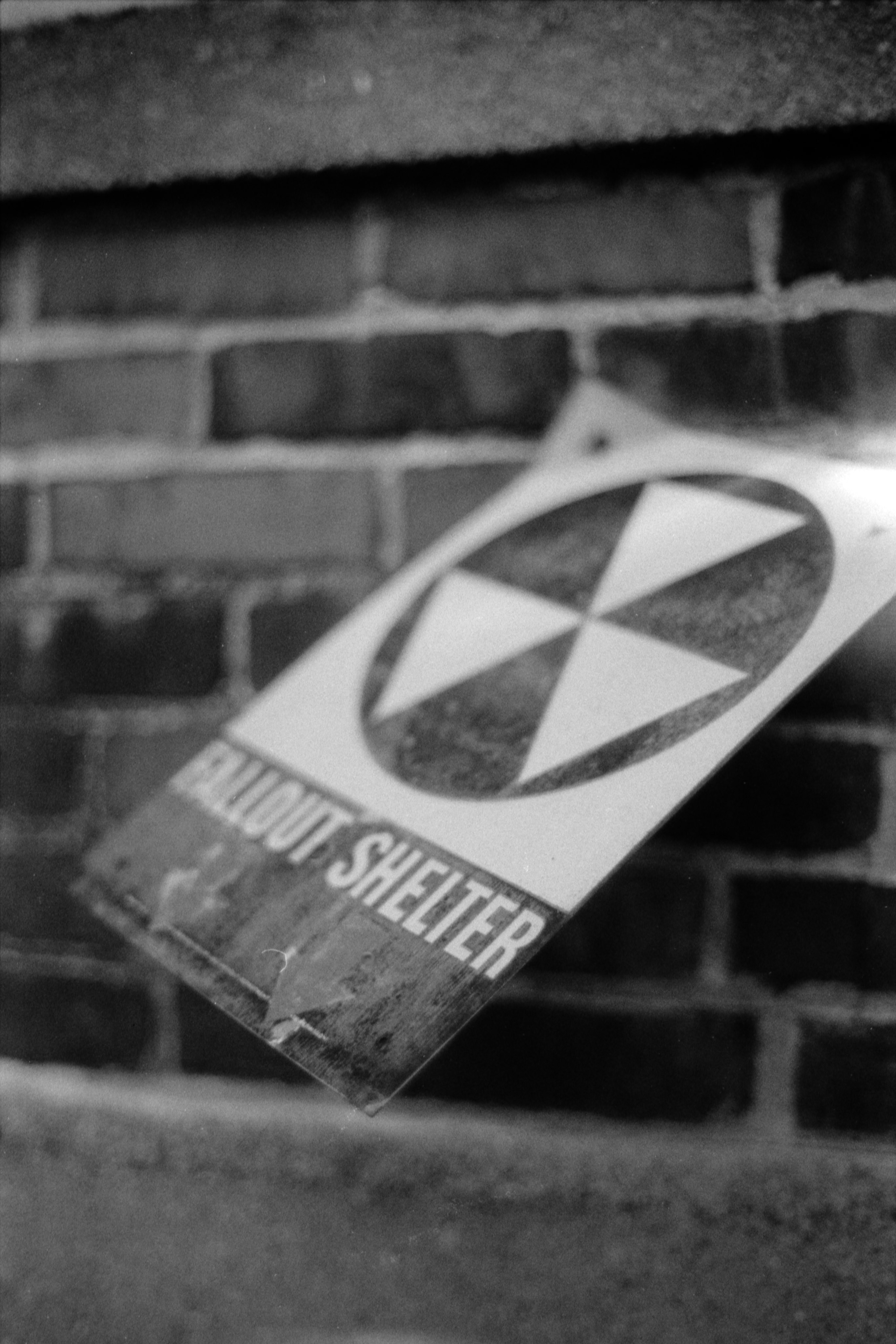 Faded fallout shelter sign leaning against a brick wall, showcasing wear and historical significance.