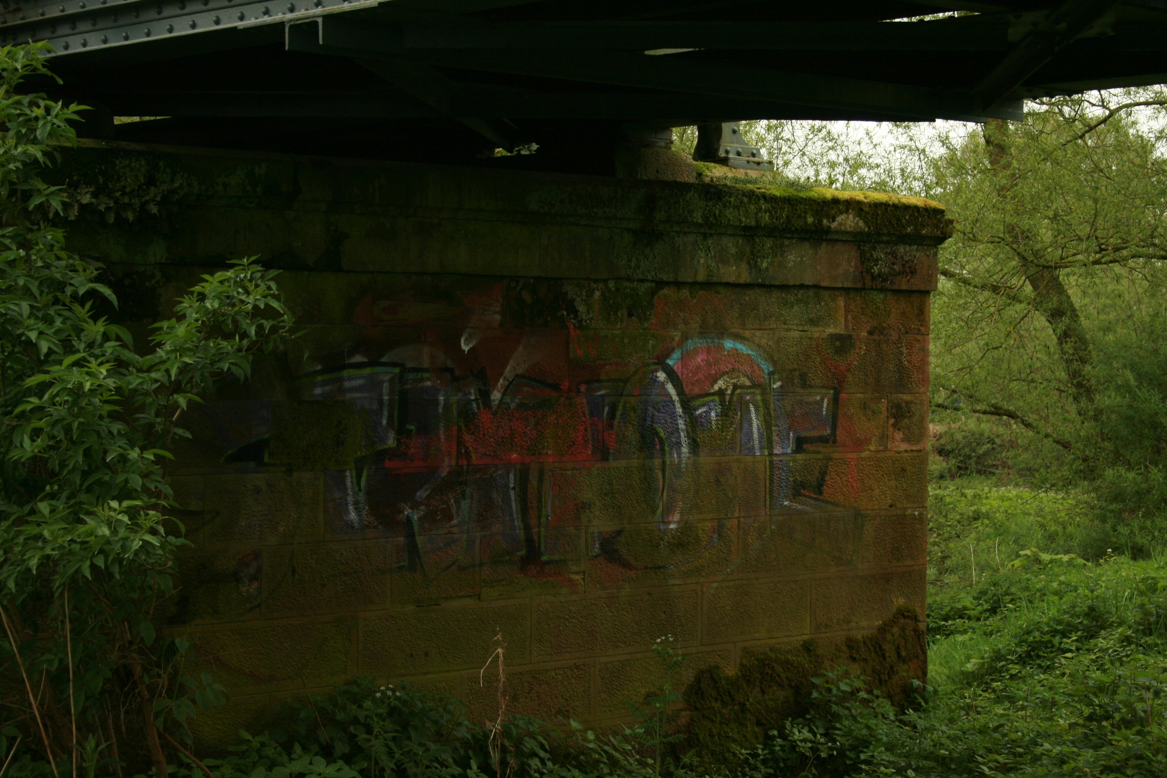 Mossy Brick Canvas: Graffiti Under a Weathered Bridge